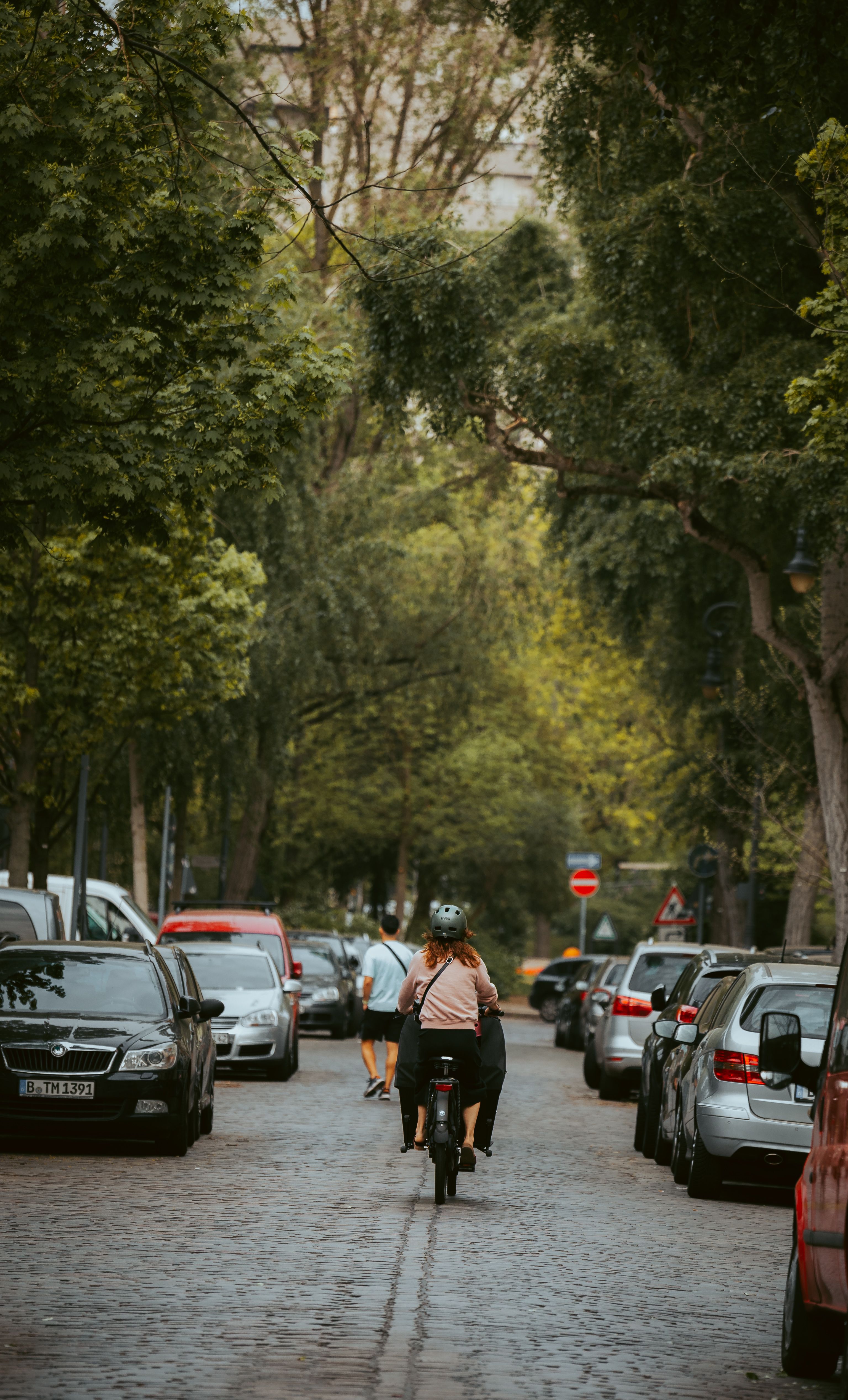 Back View of a Cyclist Riding between Cars on an Alley · Free Stock Photo