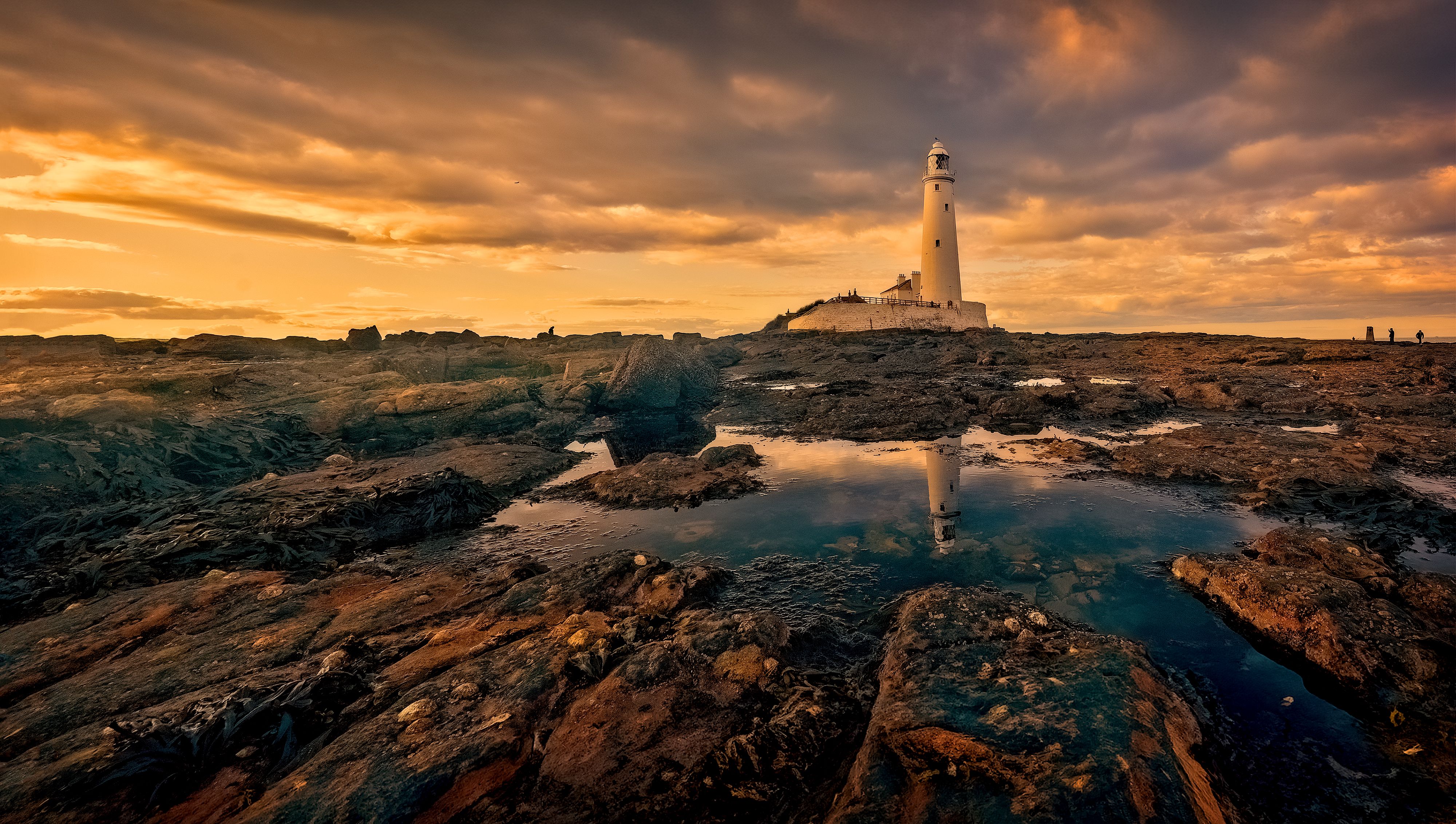 A lighthouse sits on a rocky shore at sunset · Free Stock Photo
