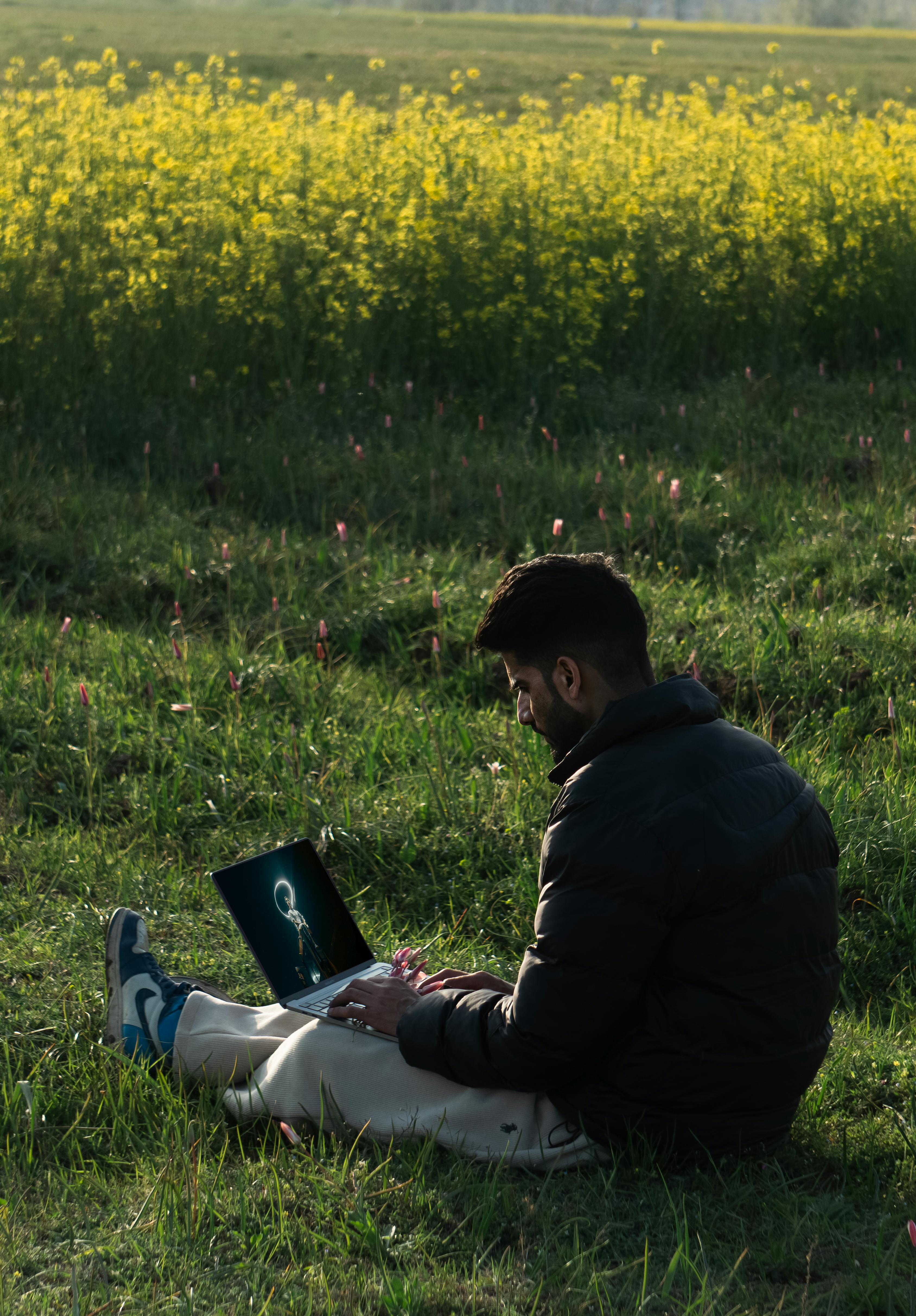 Man Sitting in Field Working on Laptop · Free Stock Photo