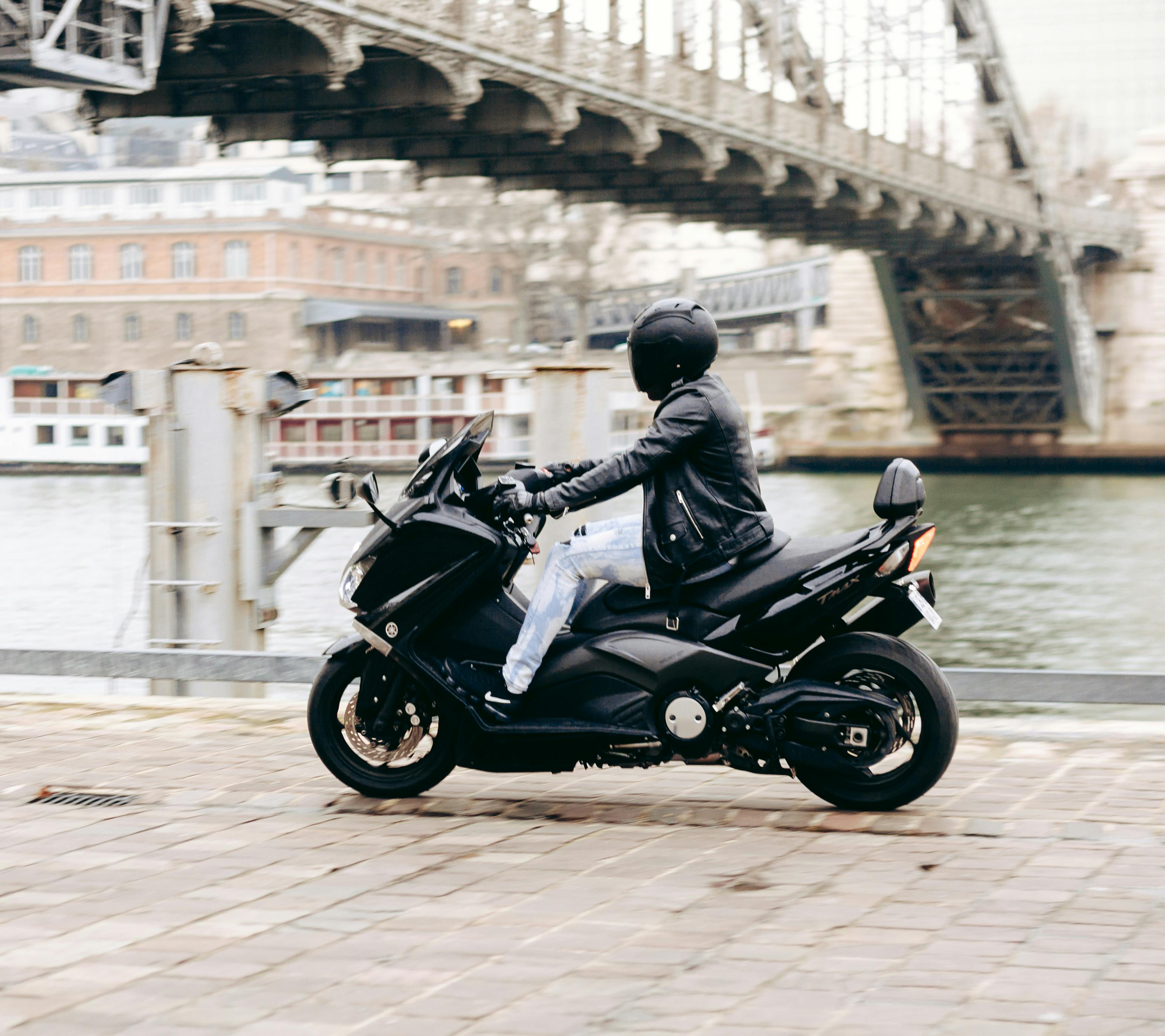 Person Riding Motor Scooter on Promenade by River · Free Stock Photo