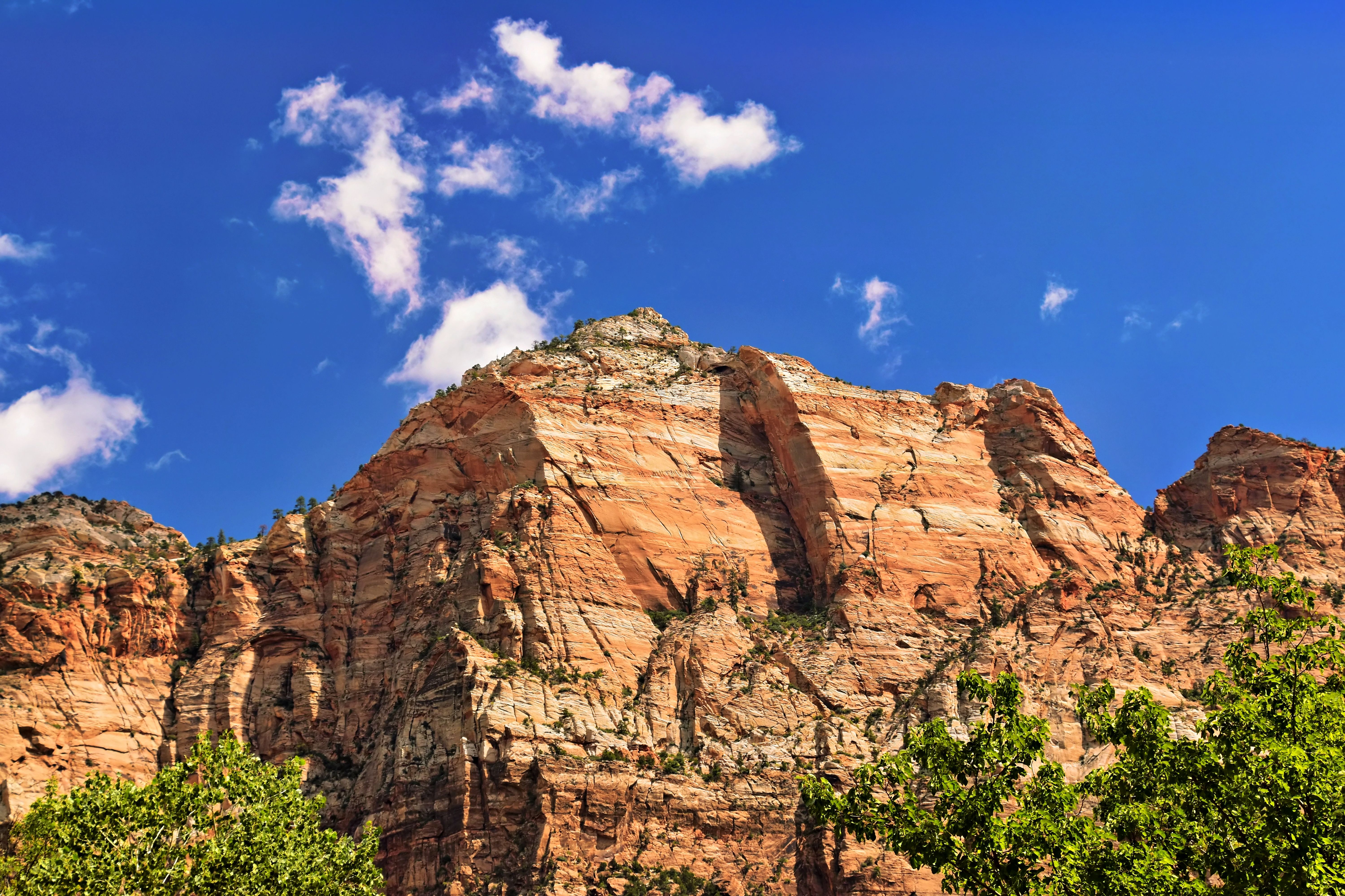 A large rock formation with trees and clouds · Free Stock Photo
