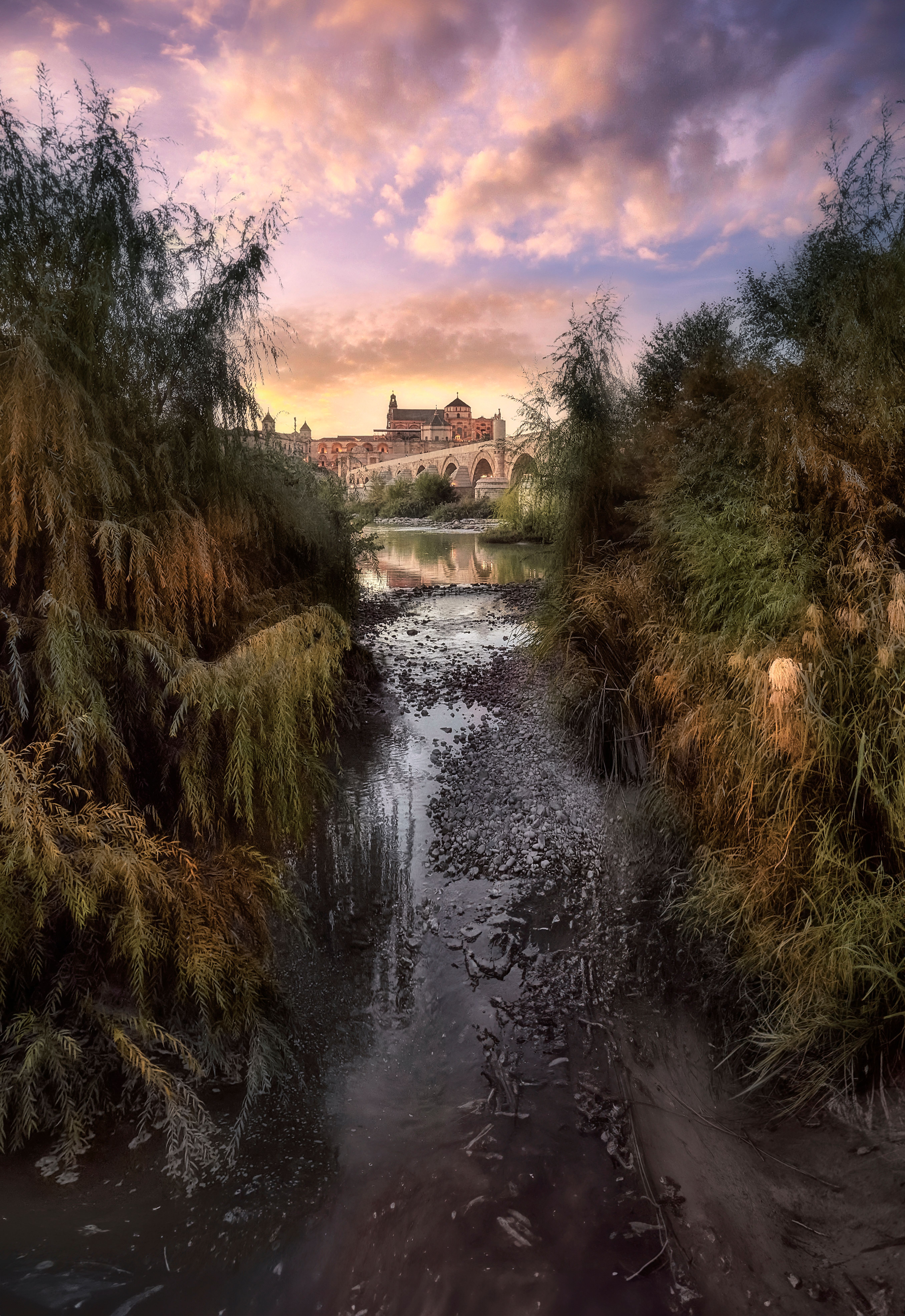 A tree lined dried stream with arch bridge and old buildings in the ...