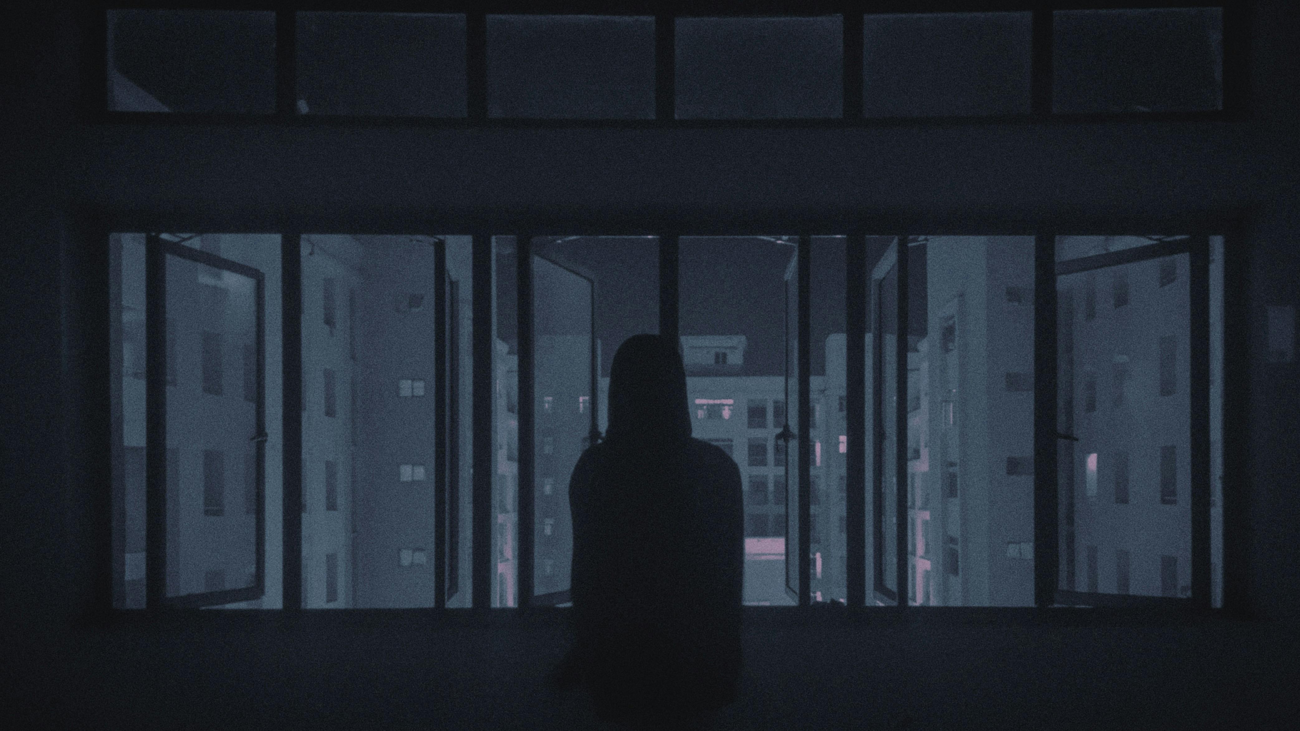 Silhouette of a Person Standing by the Window with View of Buildings in ...