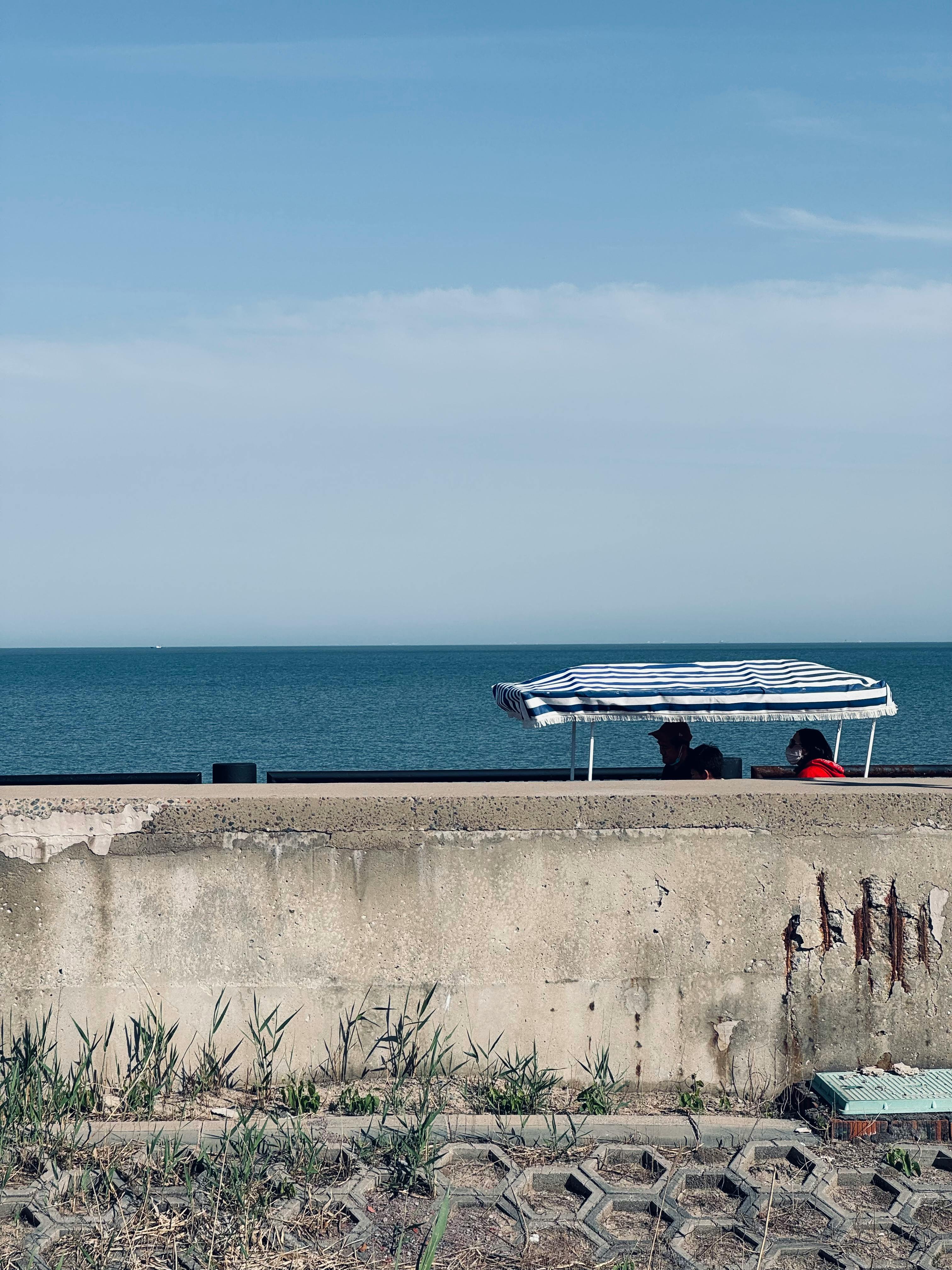 People under Cover behind Wall on Sea Shore · Free Stock Photo