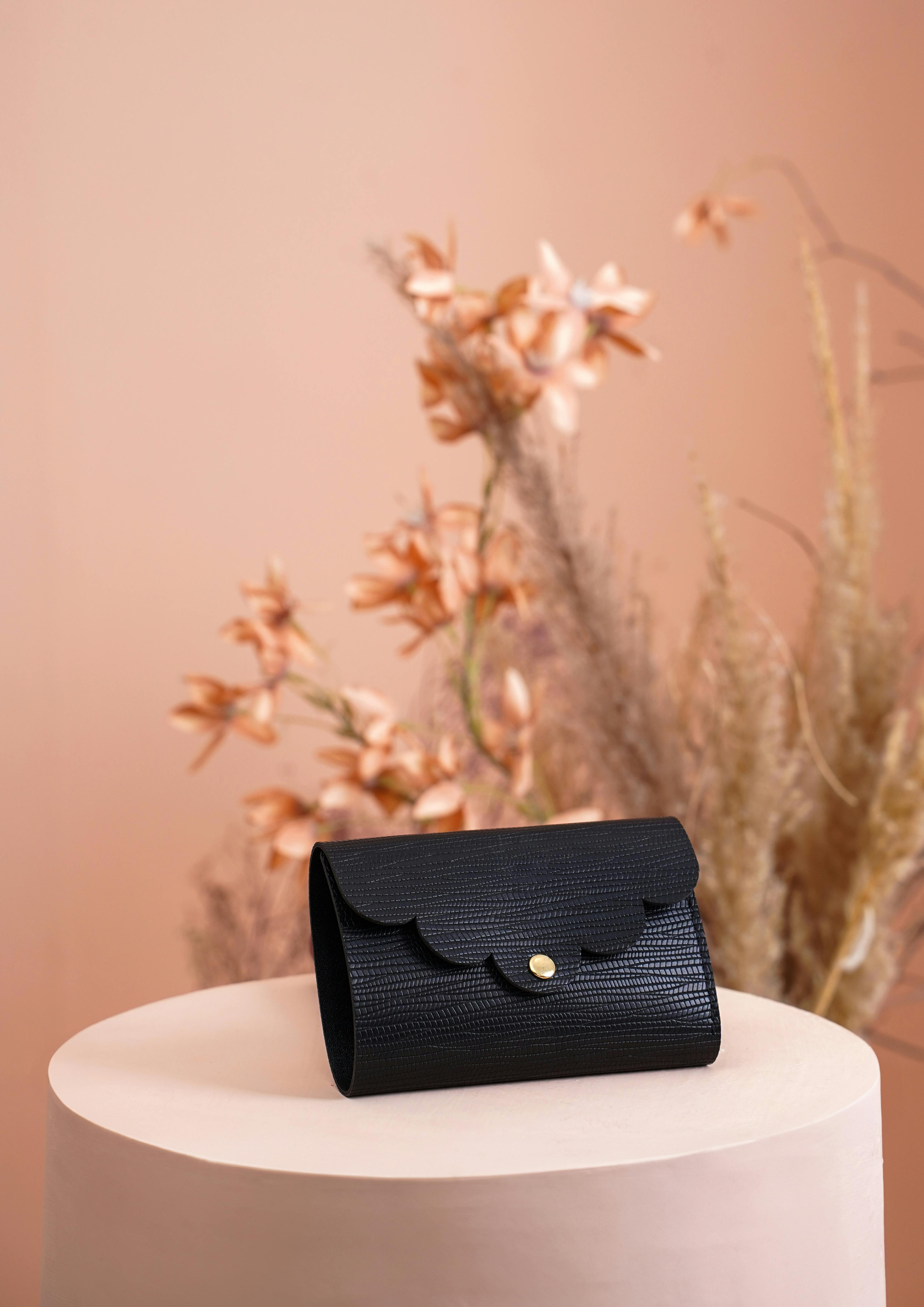 A Black Purse Lying on the Background of Flowers · Free Stock Photo