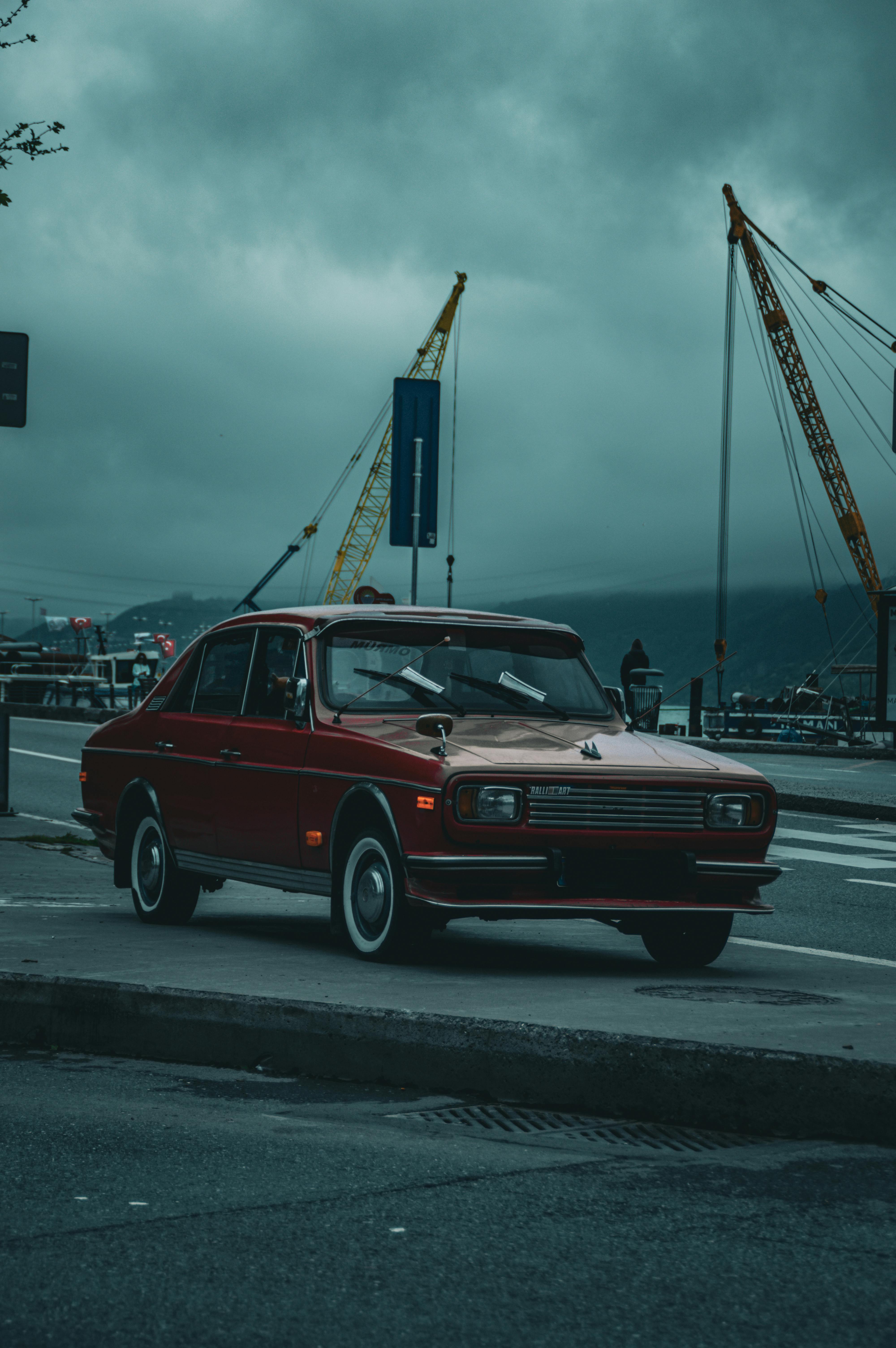 A red car parked on the street next to a crane · Free Stock Photo
