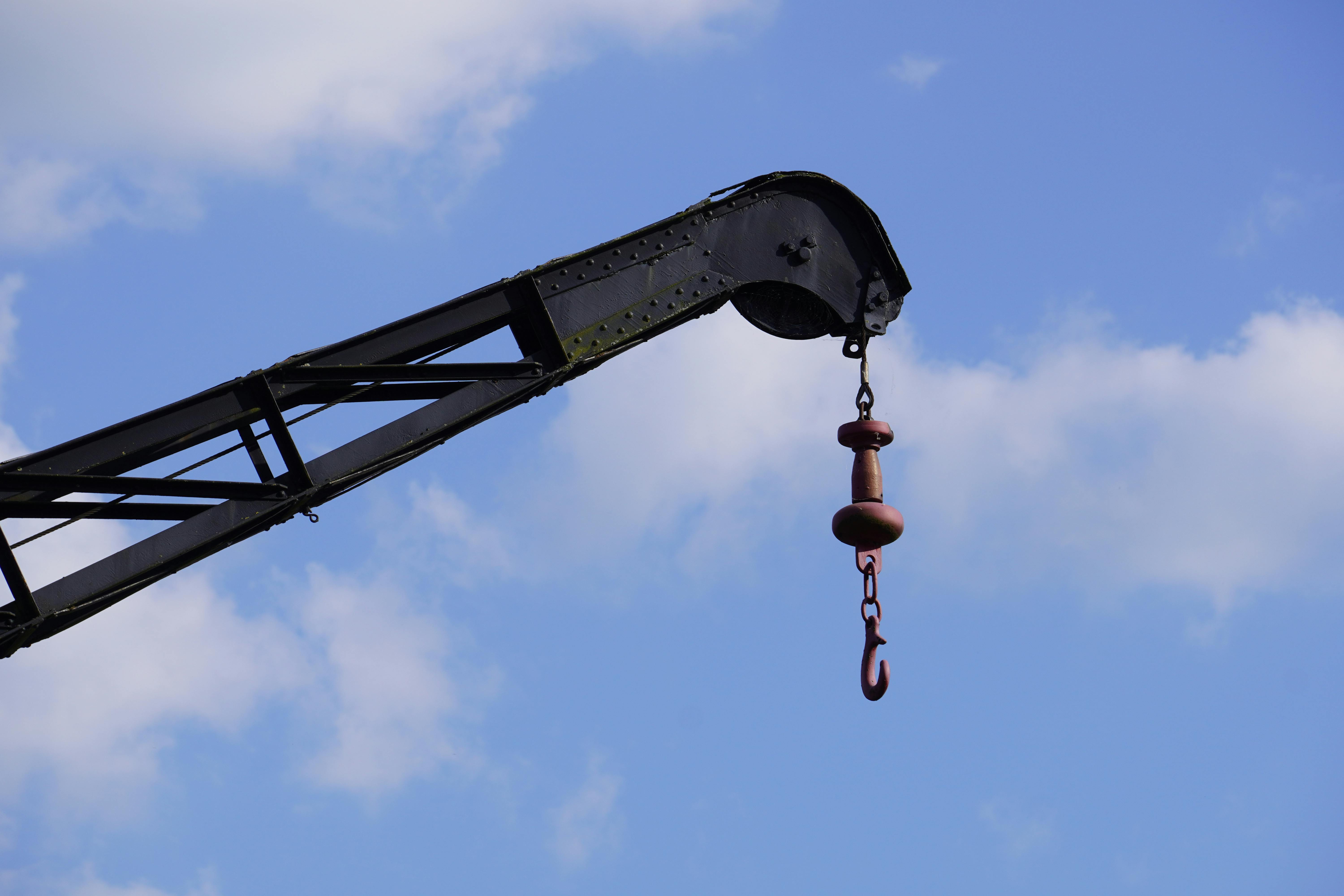 A crane lifting a large object against a blue sky · Free Stock Photo