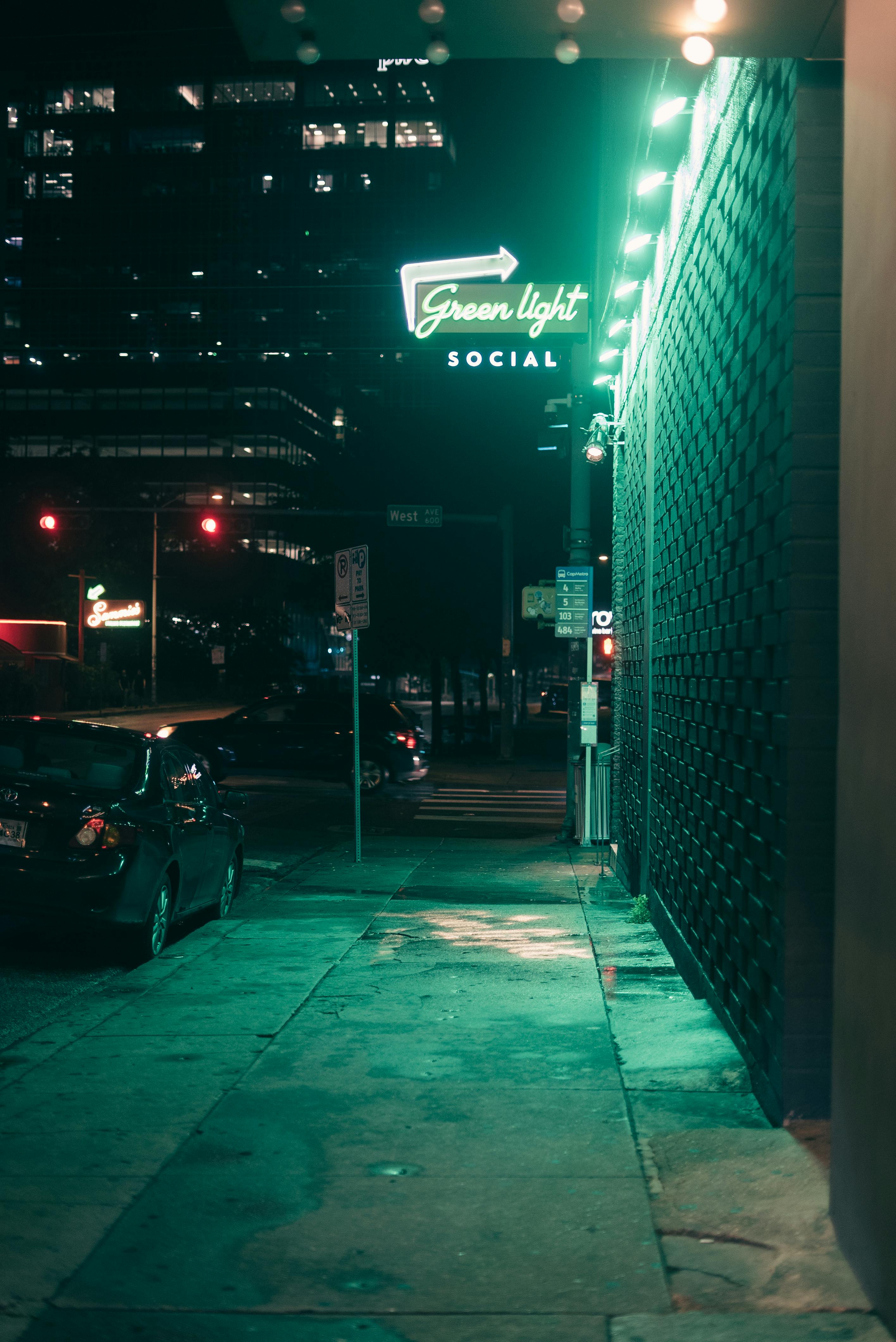 Neon Sign of the Green Light Social Bar Above the Sidewalk at Night ...