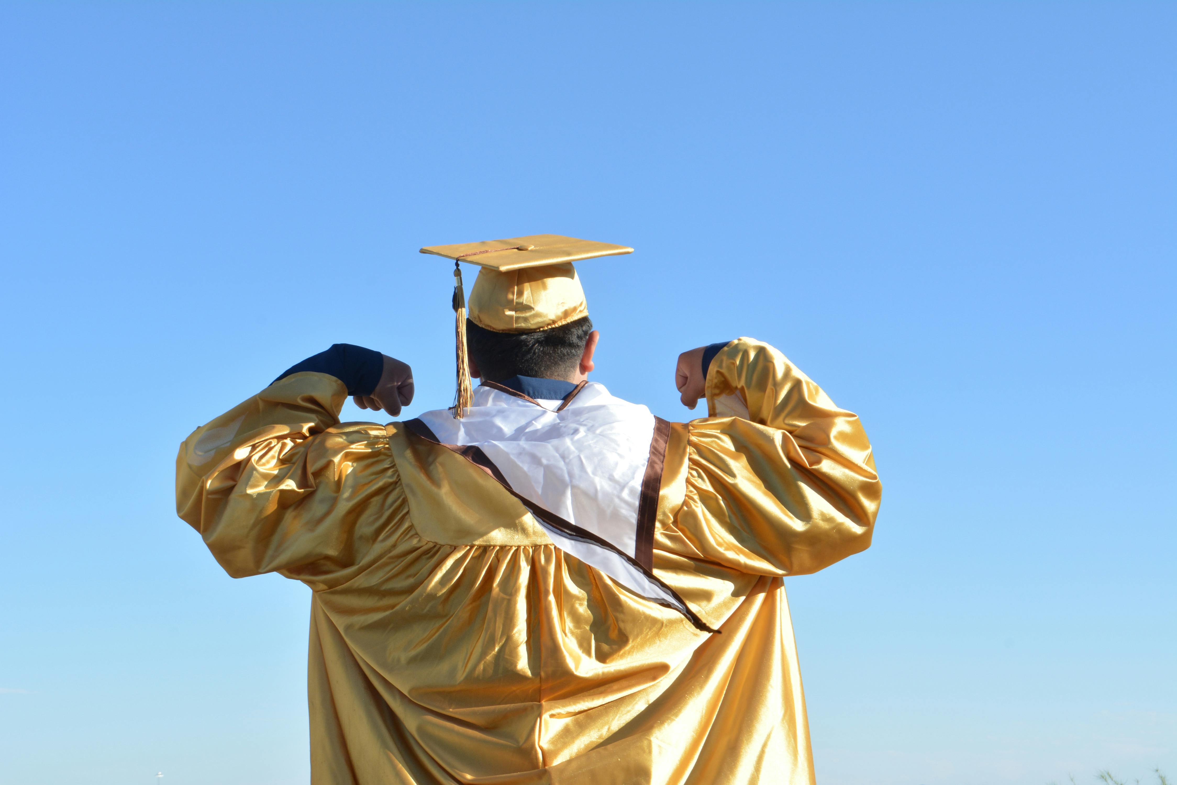 Man in Gold Graduation Gown Standing against Blue Sky · Free Stock Photo