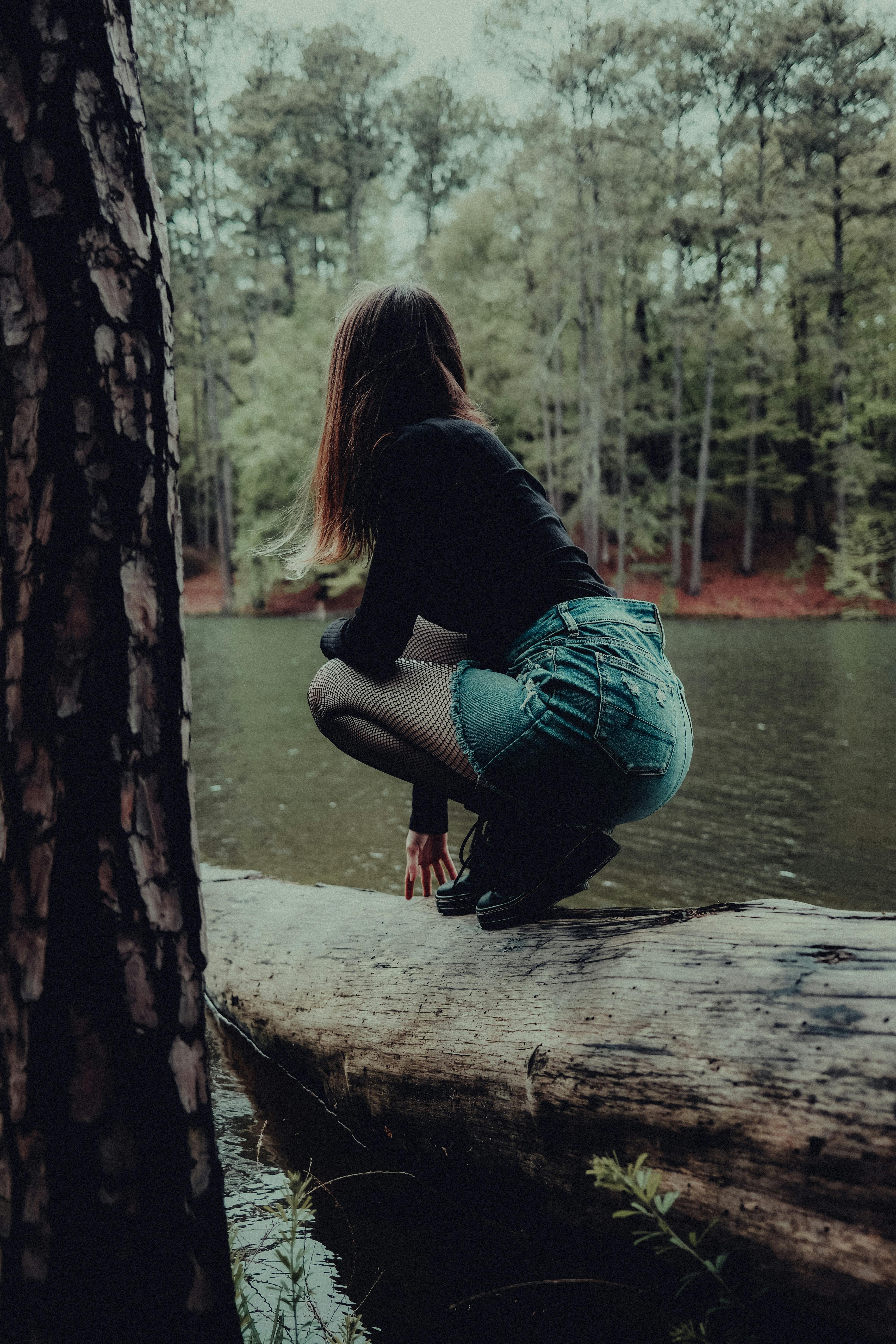 Rear View of a Woman Crouching on a Log by the River · Free Stock Photo