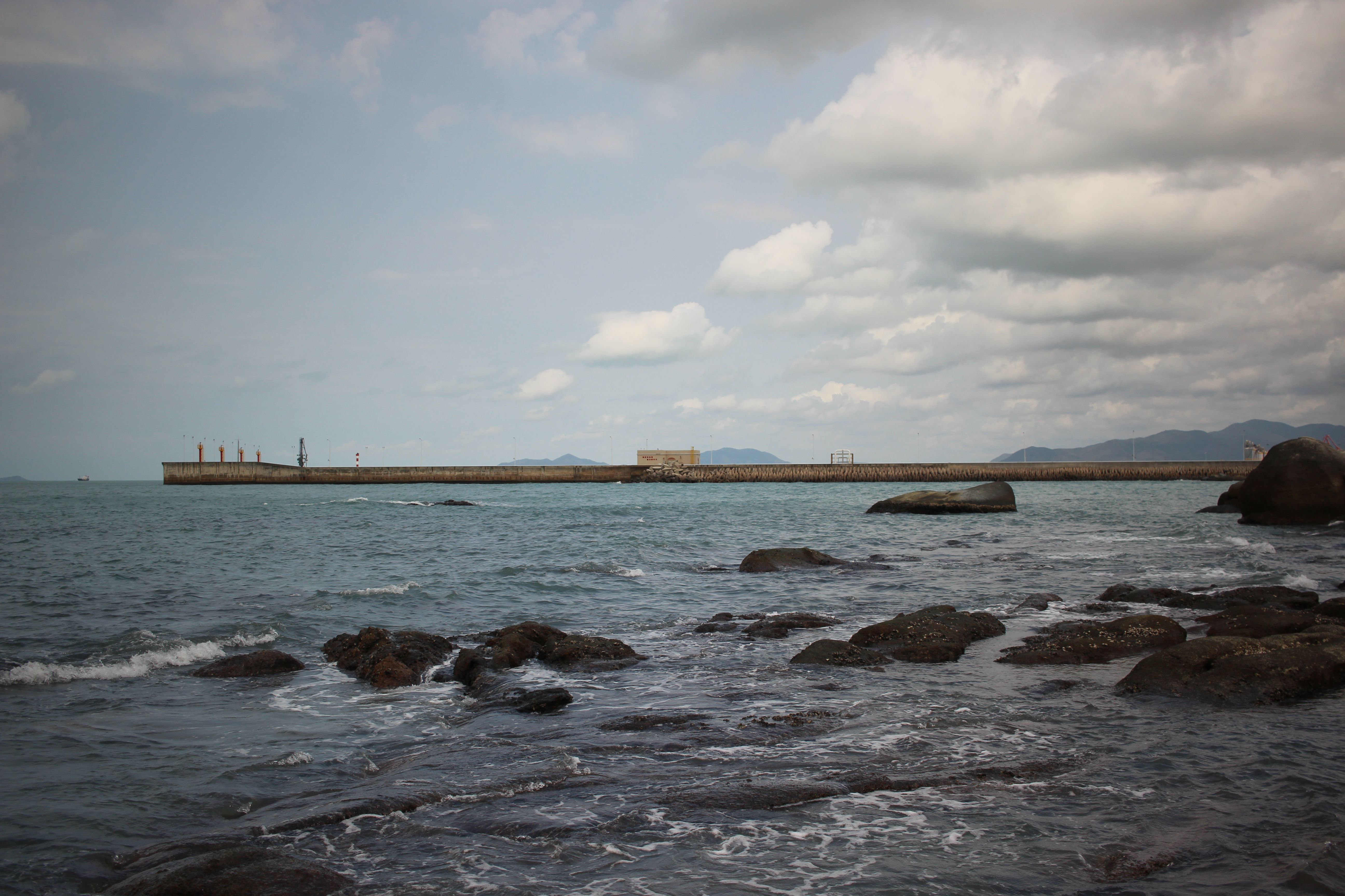 Rocks on Sea Shore and Pier behind · Free Stock Photo