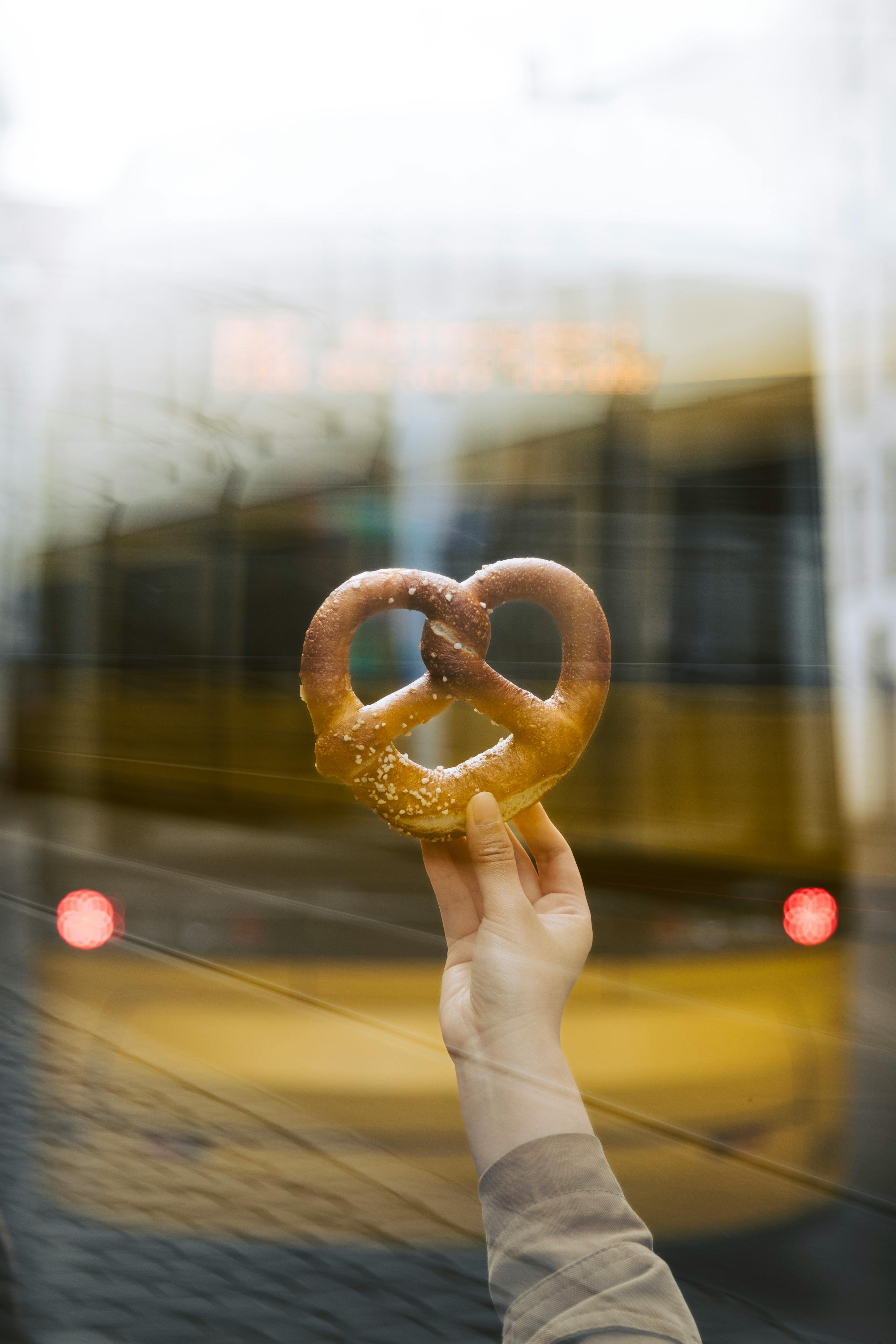 Hand Holding Pretzel next to Train Reflection in Window · Free Stock Photo
