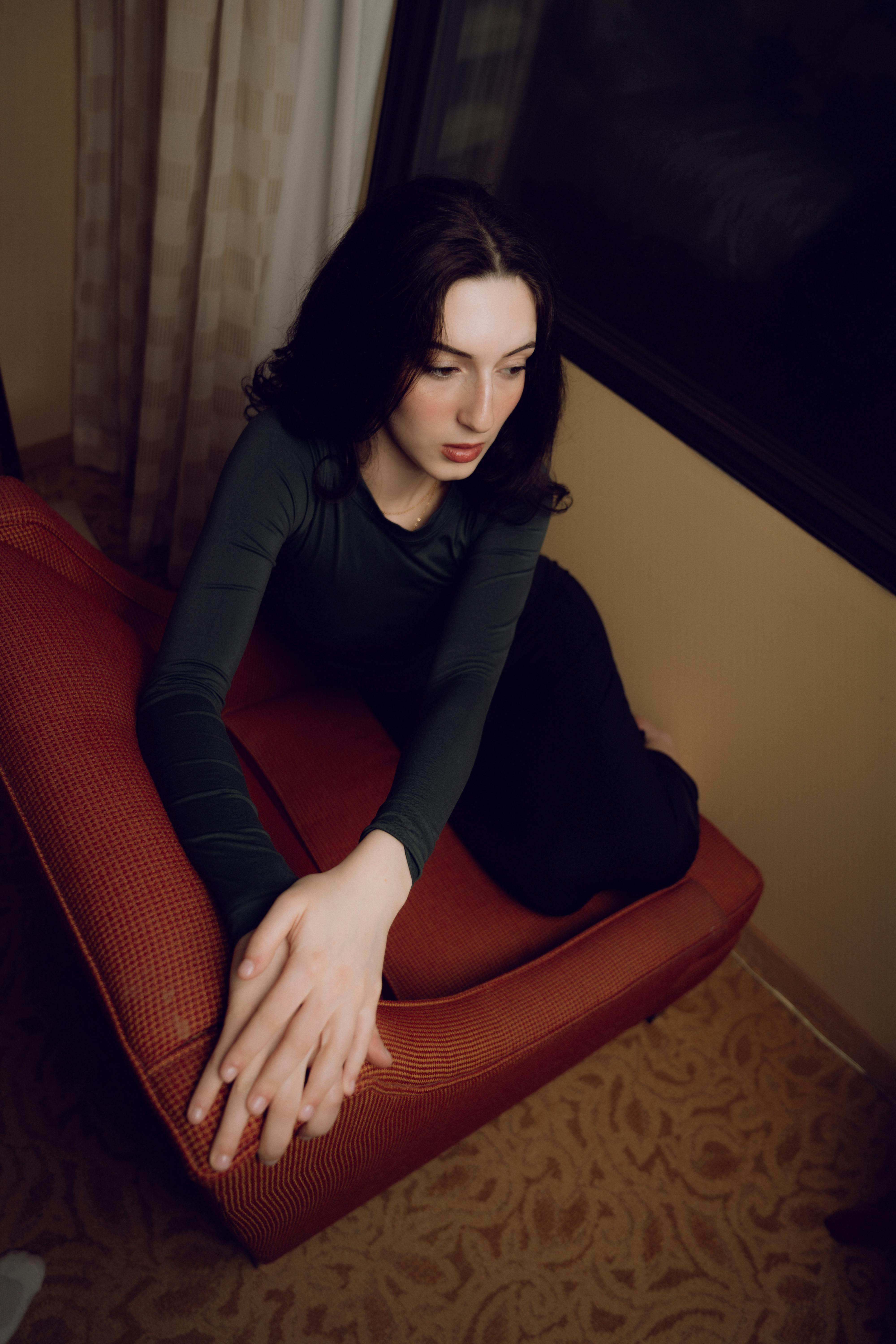 A woman sitting on a red chair with her hands on her lap · Free Stock Photo