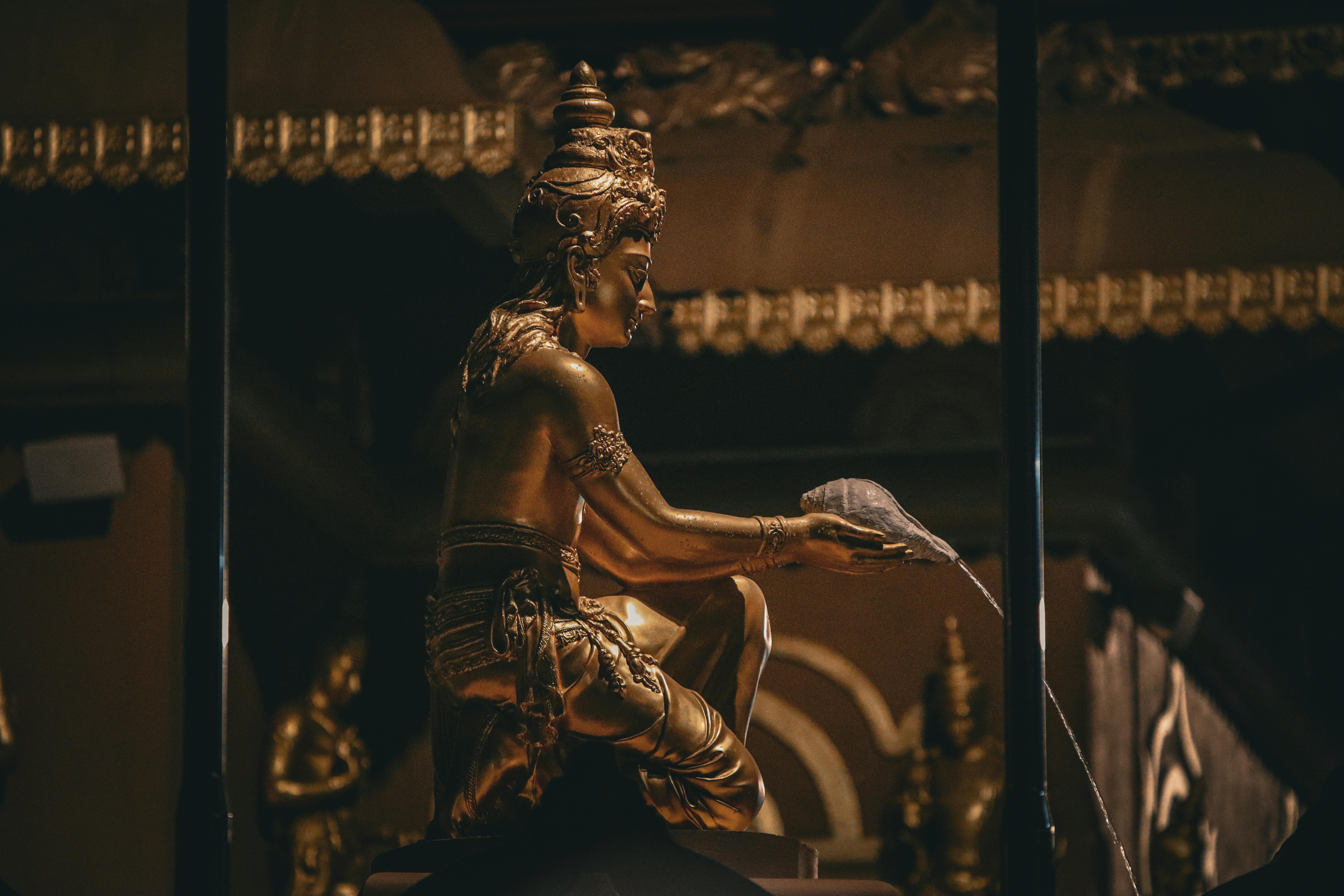 A statue of a golden god holding a cup · Free Stock Photo