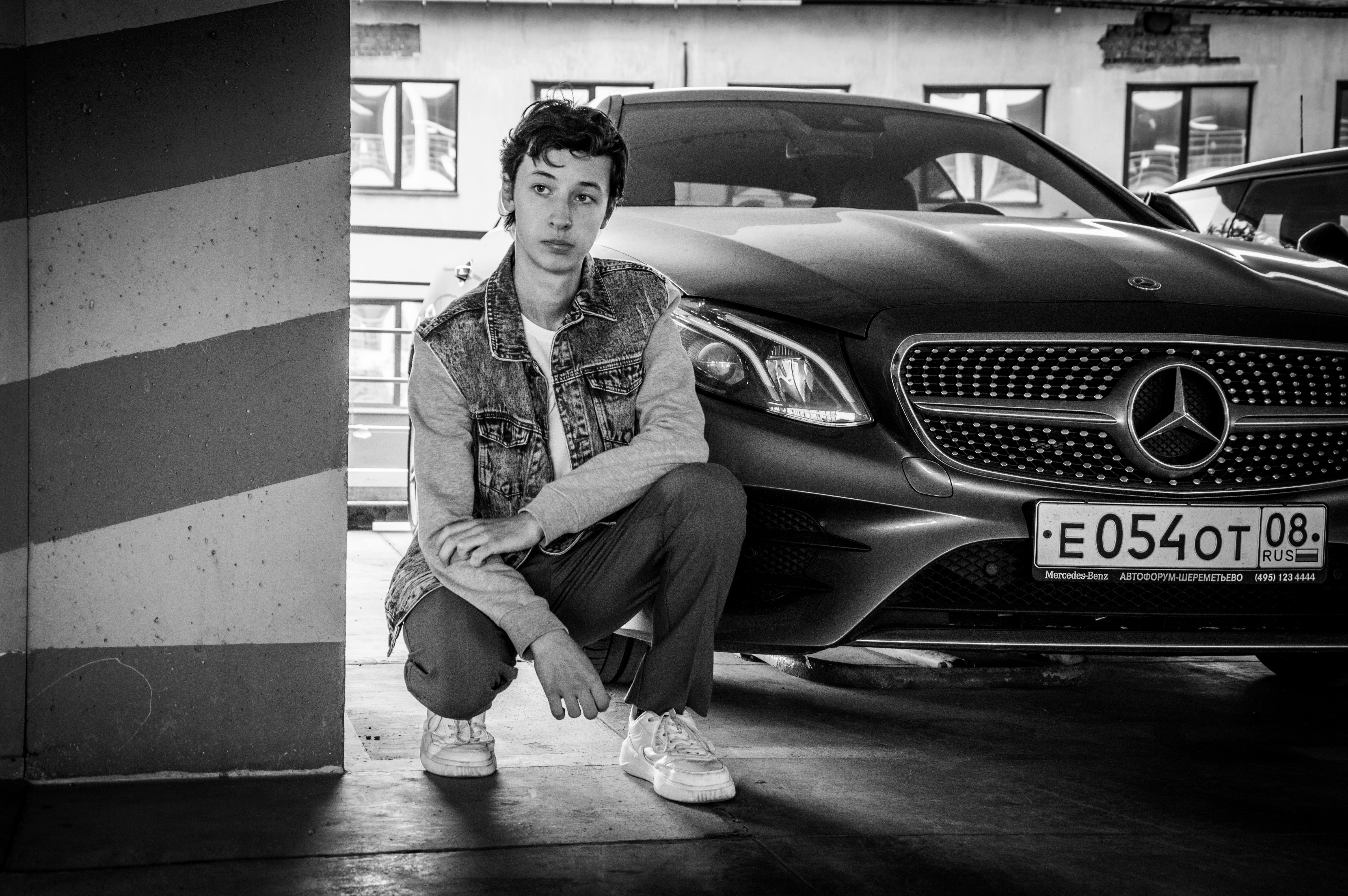 Young Man Crouching in Front of a Parked Mercedes Car · Free Stock Photo