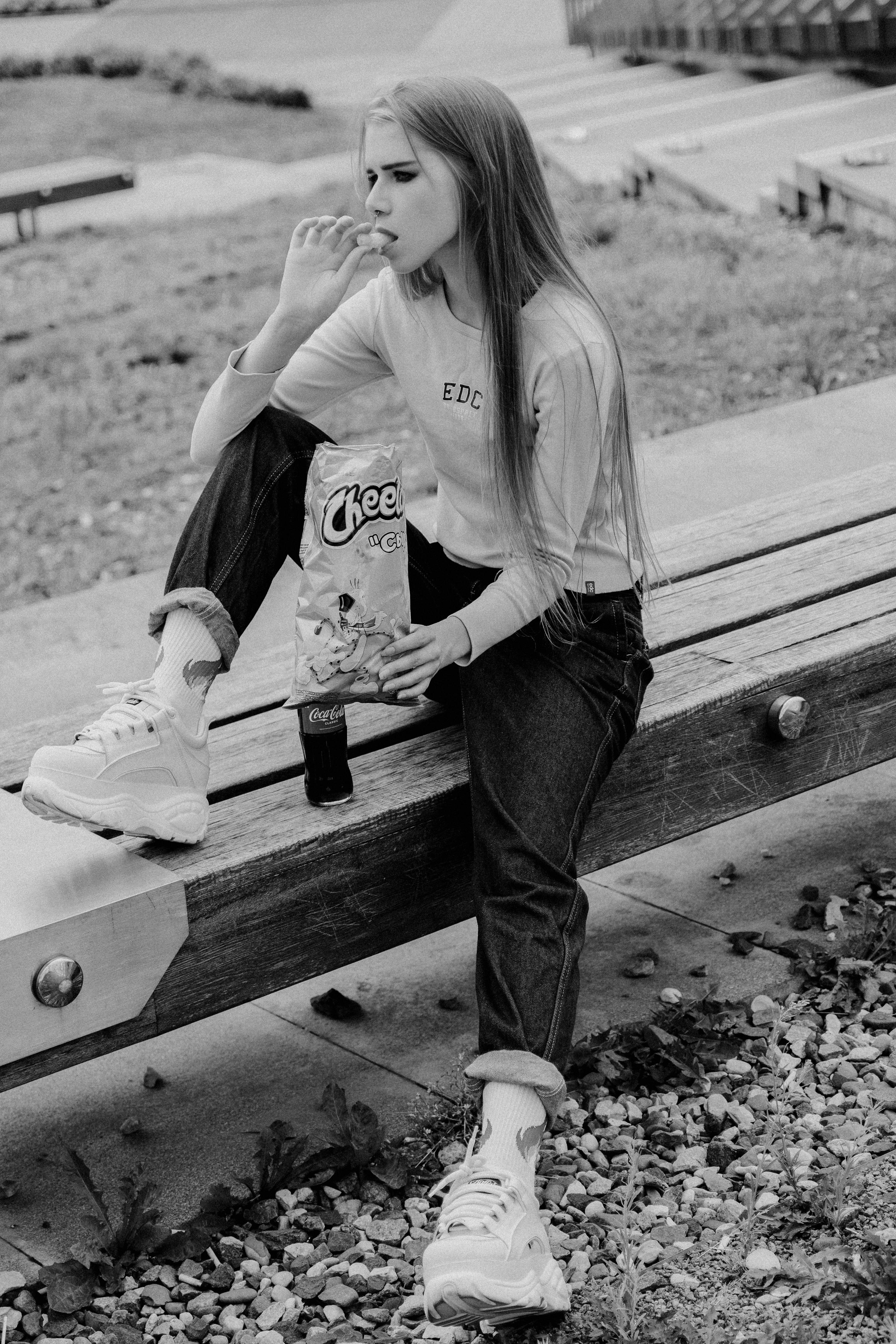 Long-Haired Girl Sitting on a Bench Eating Cheetos · Free Stock Photo