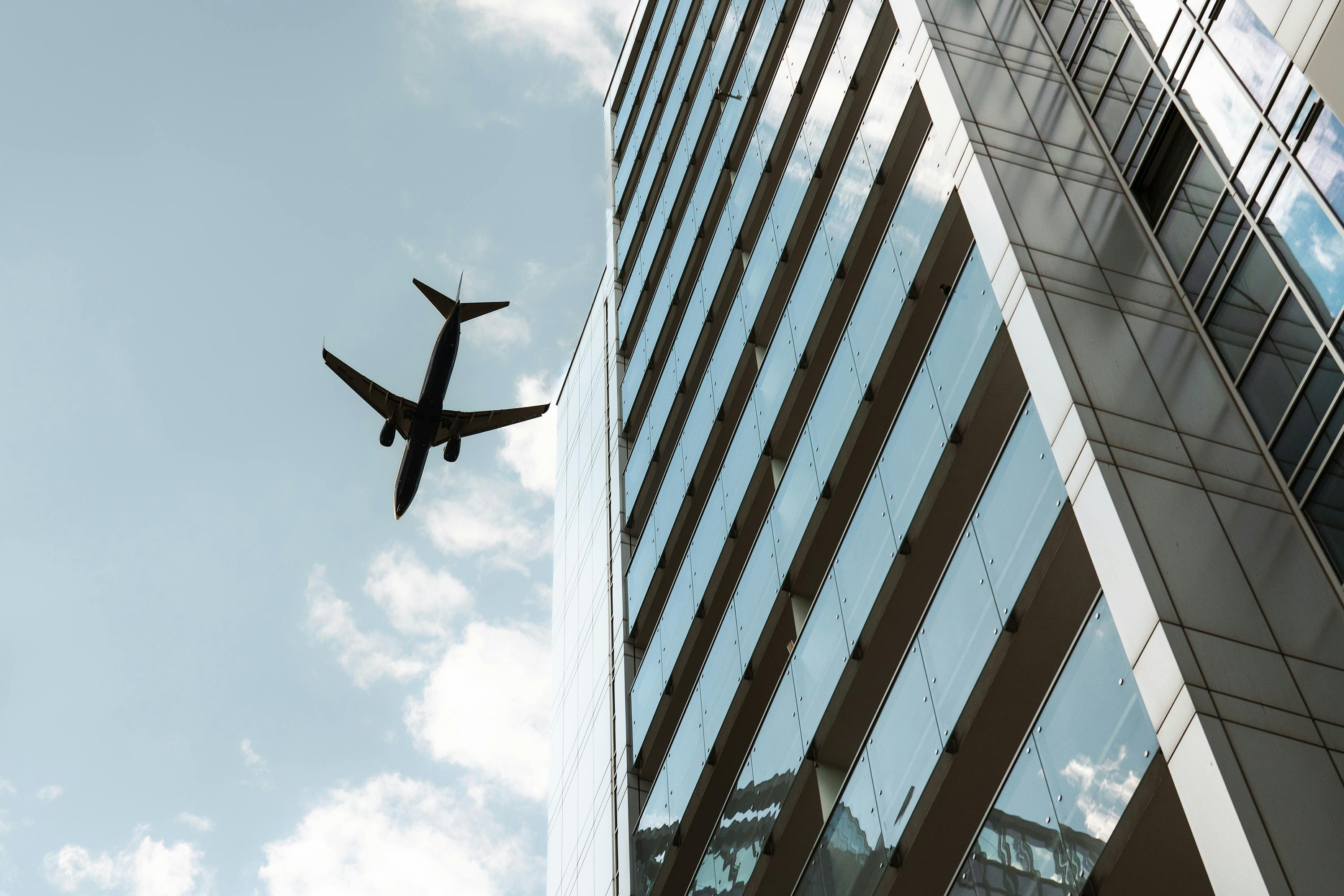 Plane Flying Above Glass Building · Free Stock Photo