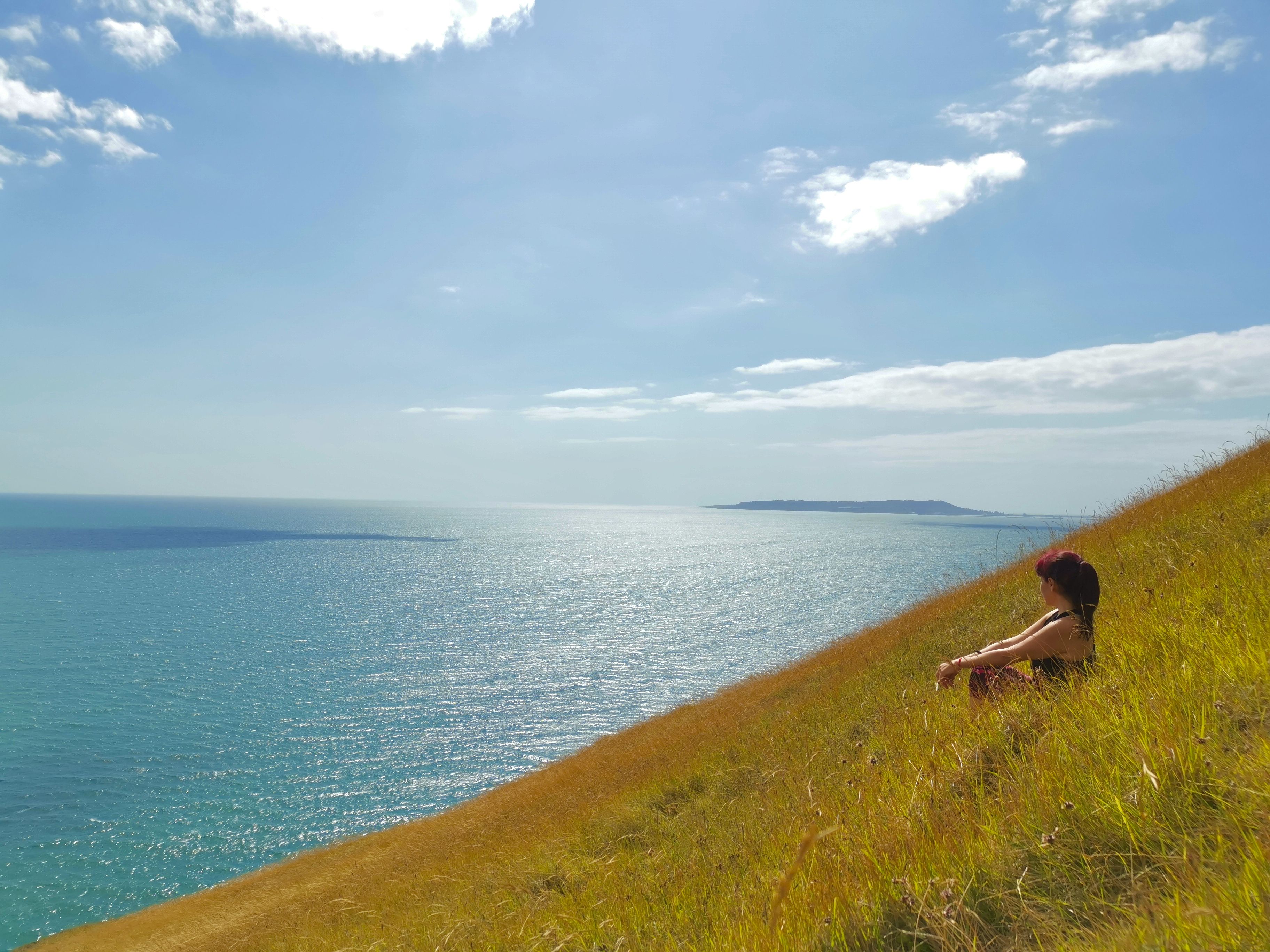 A person sitting on a hill overlooking the ocean · Free Stock Photo
