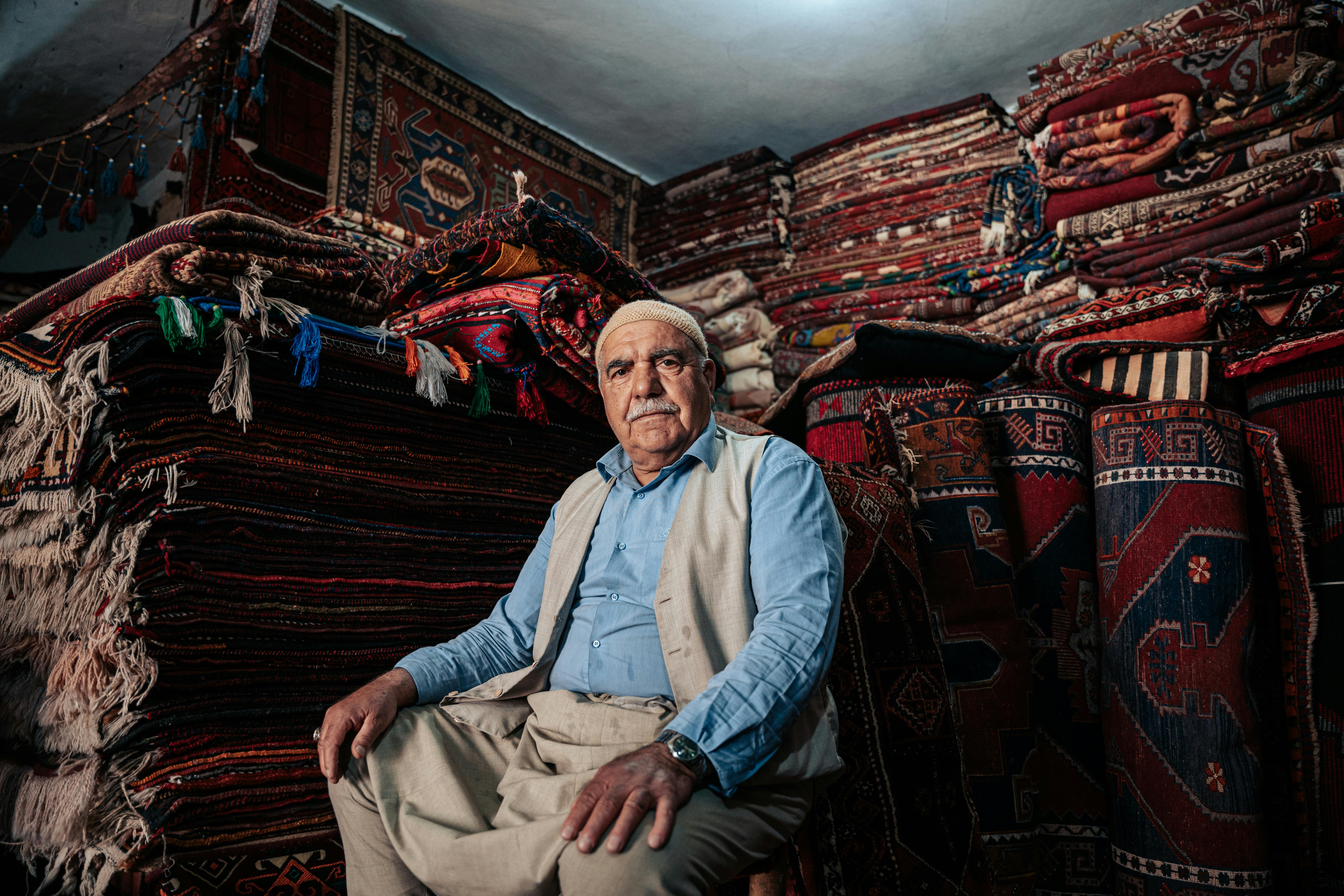 Man Sitting with Carpets behind · Free Stock Photo