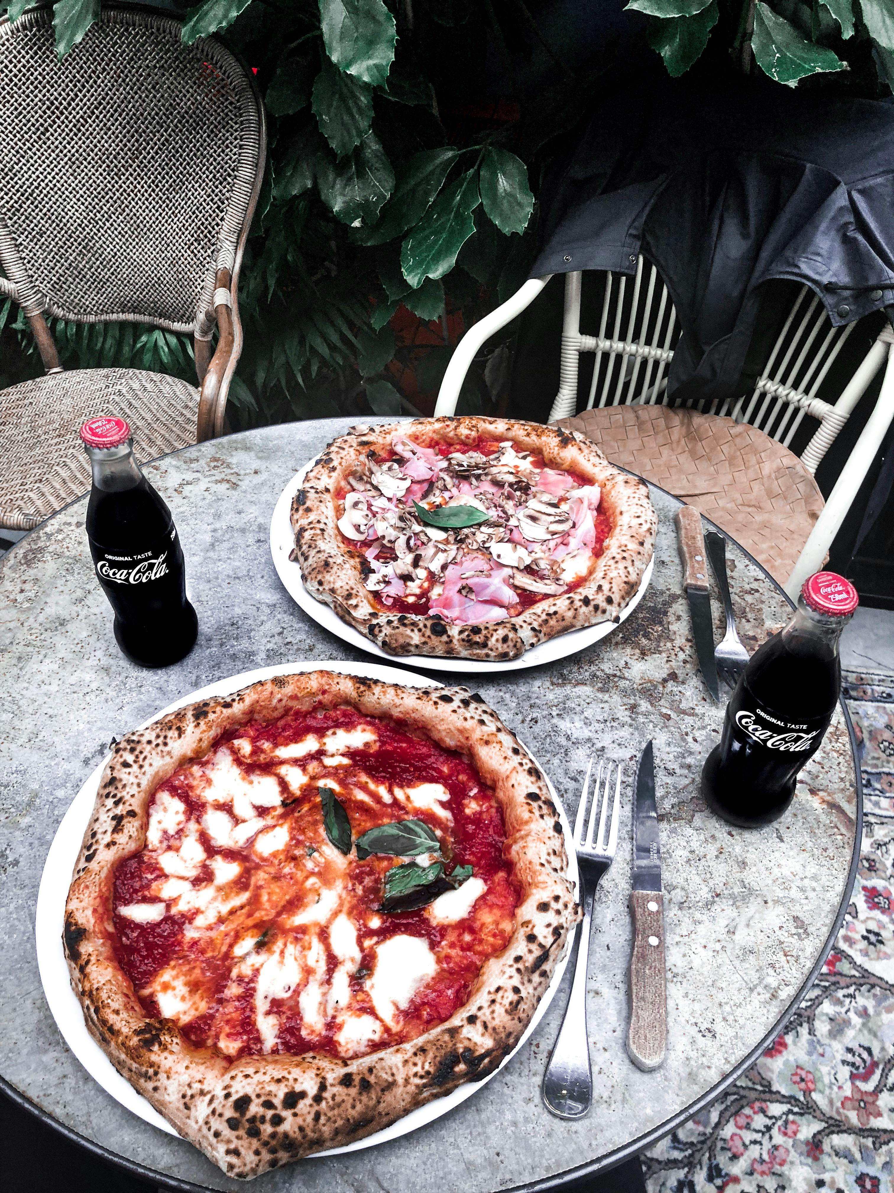 Two Pizzas on Plates, Forks and Knives and Coca Cola Sodas on top of a ...
