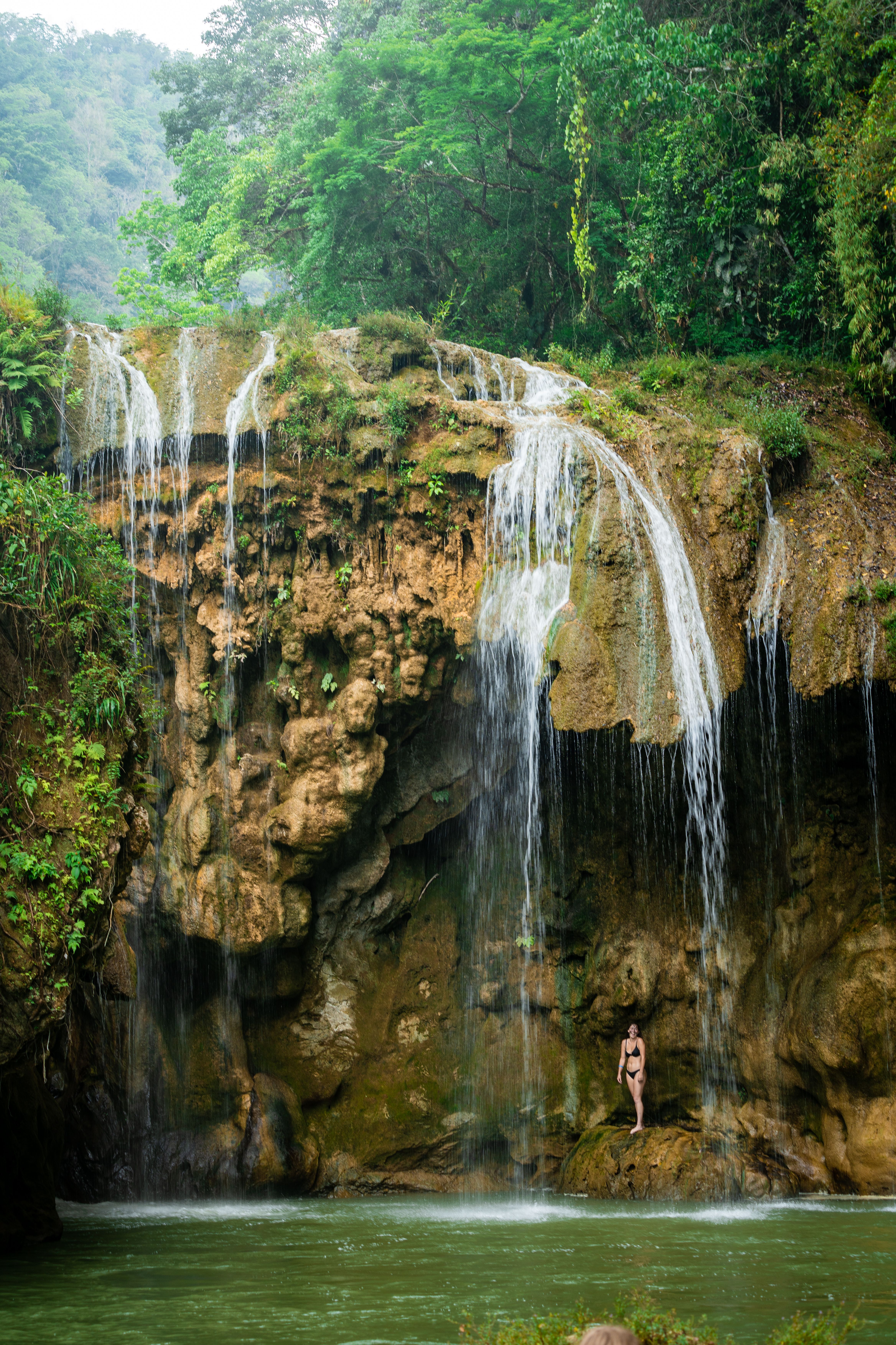 A man standing in the water at the top of a waterfall · Free Stock Photo