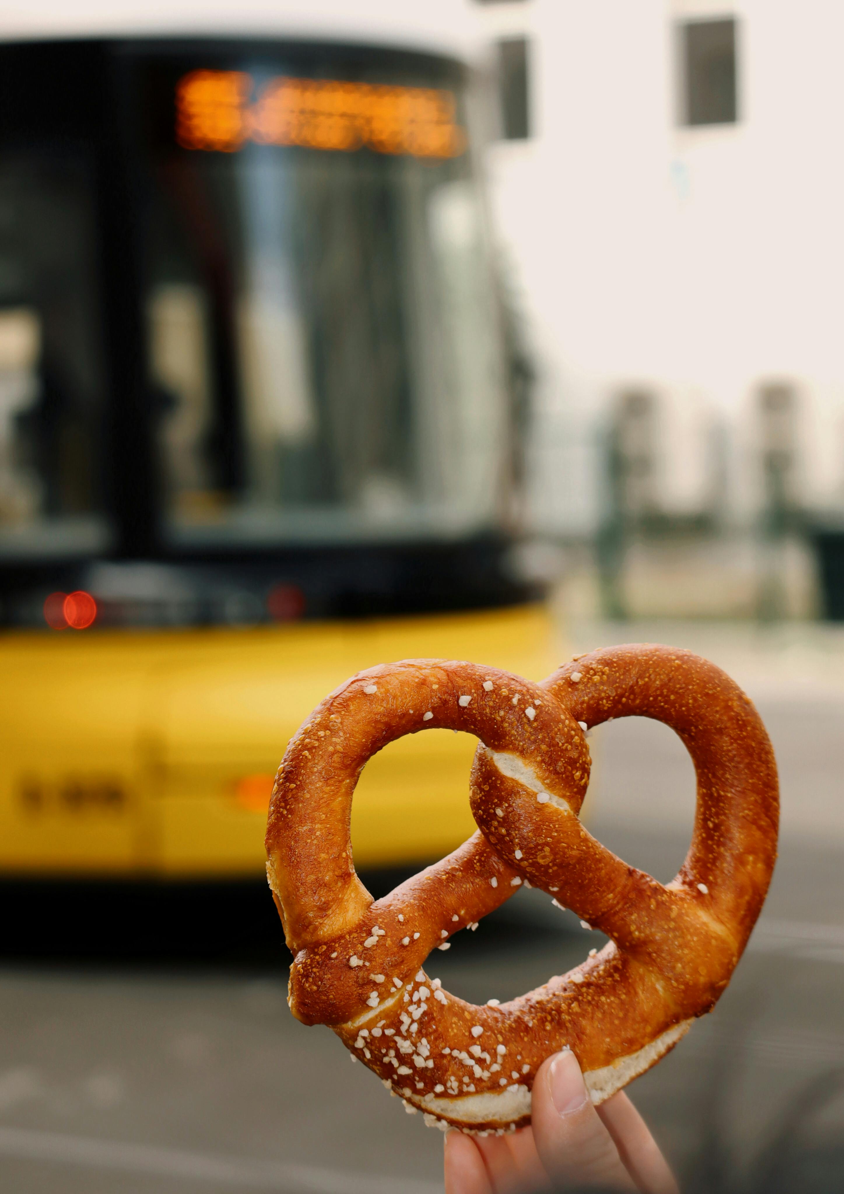 A person holding a pretzel in front of a bus · Free Stock Photo
