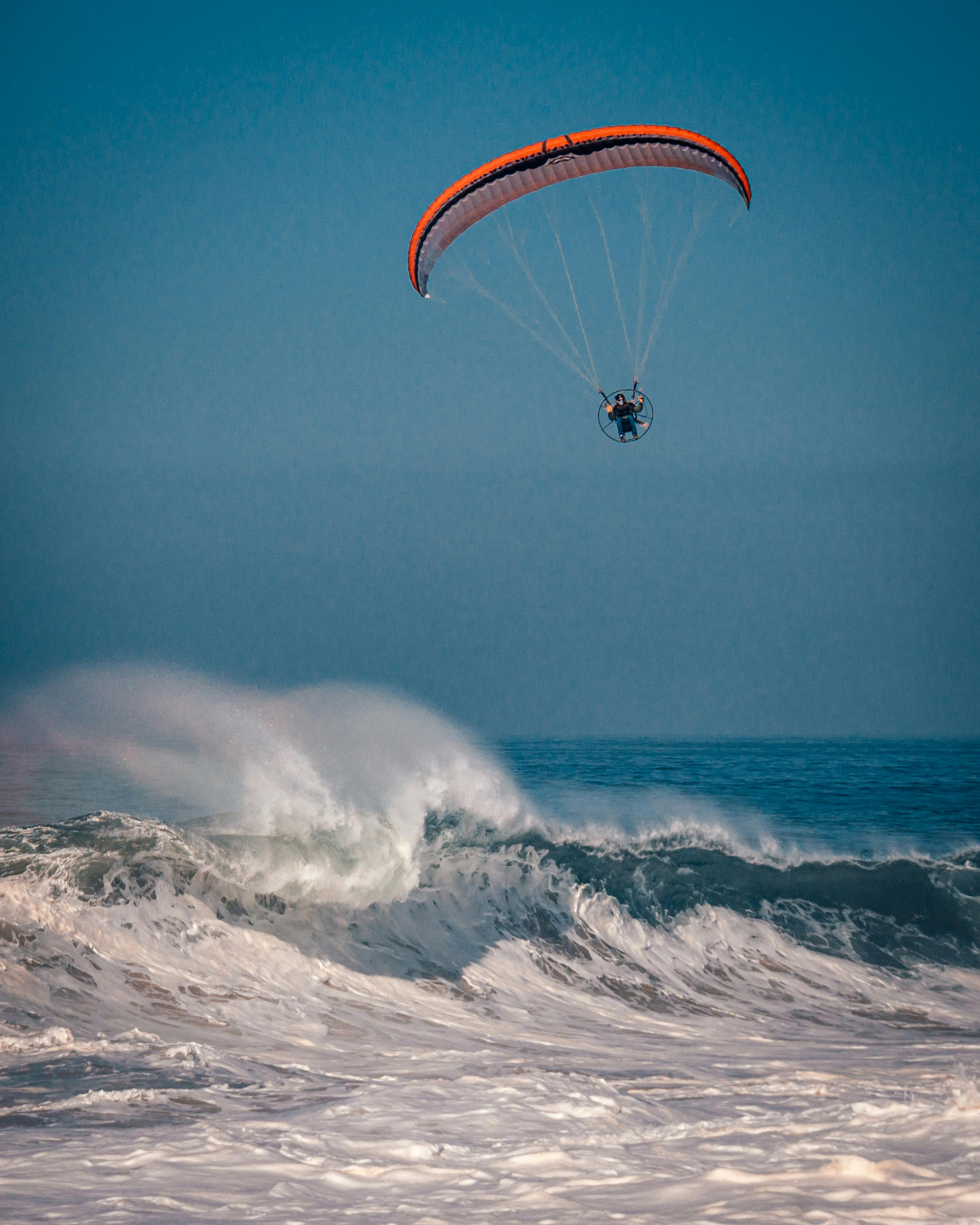 Paraglider flying over blue sea water · Free Stock Photo