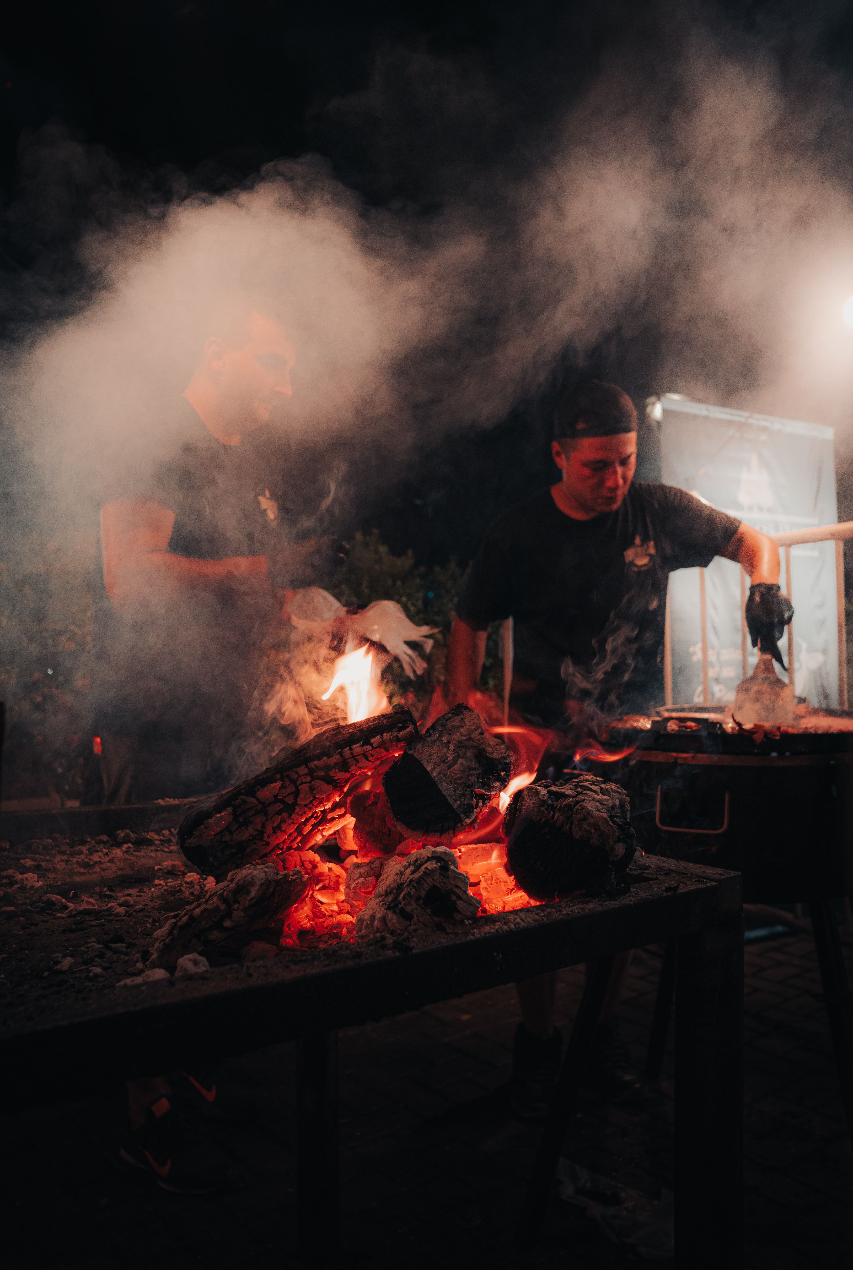 Two men cooking food on a grill at night · Free Stock Photo