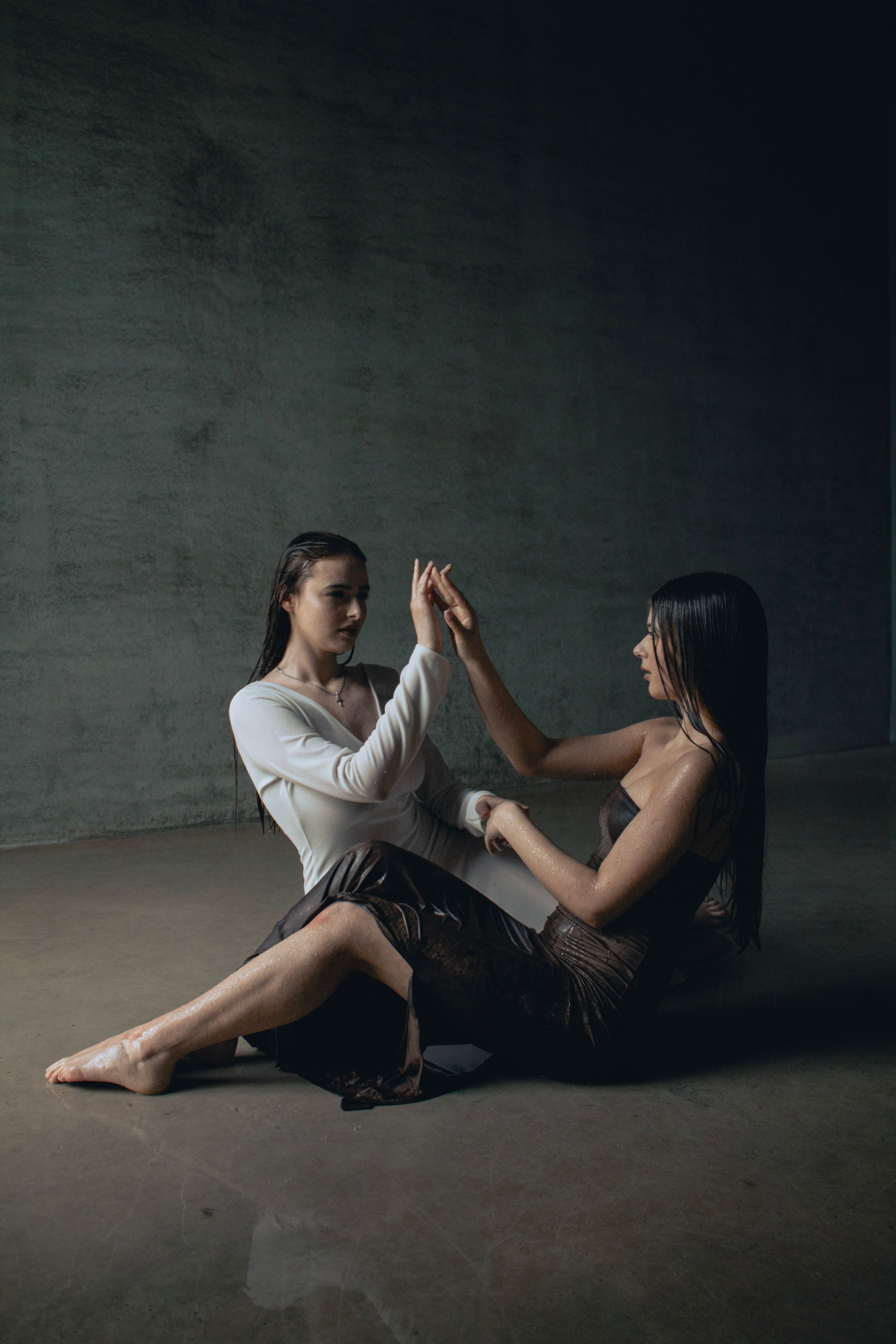 Two Young Women Touching while Sitting on a Wet Surface · Free Stock Photo