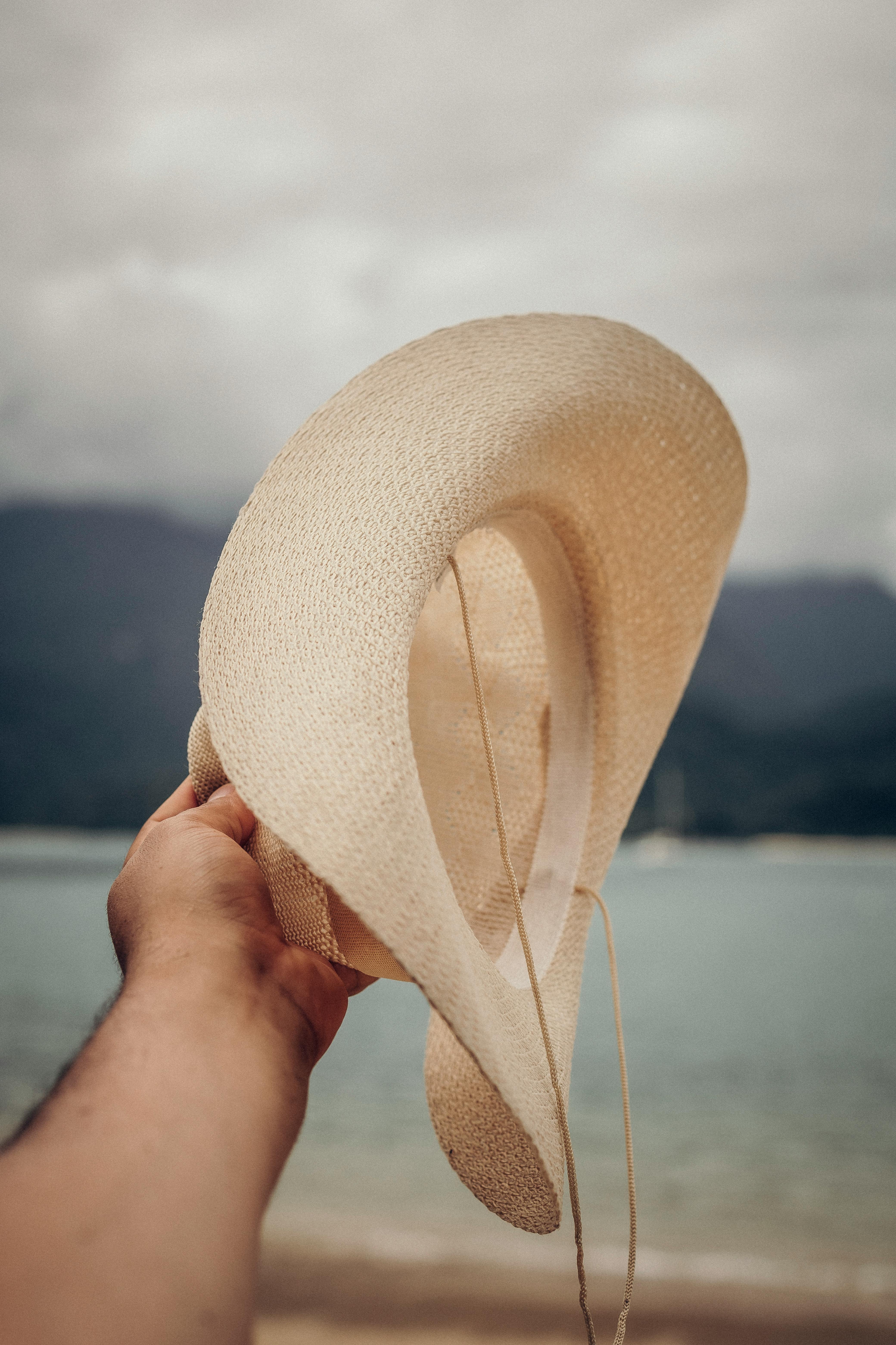 Man Hand Holding Hat on Sea Shore · Free Stock Photo