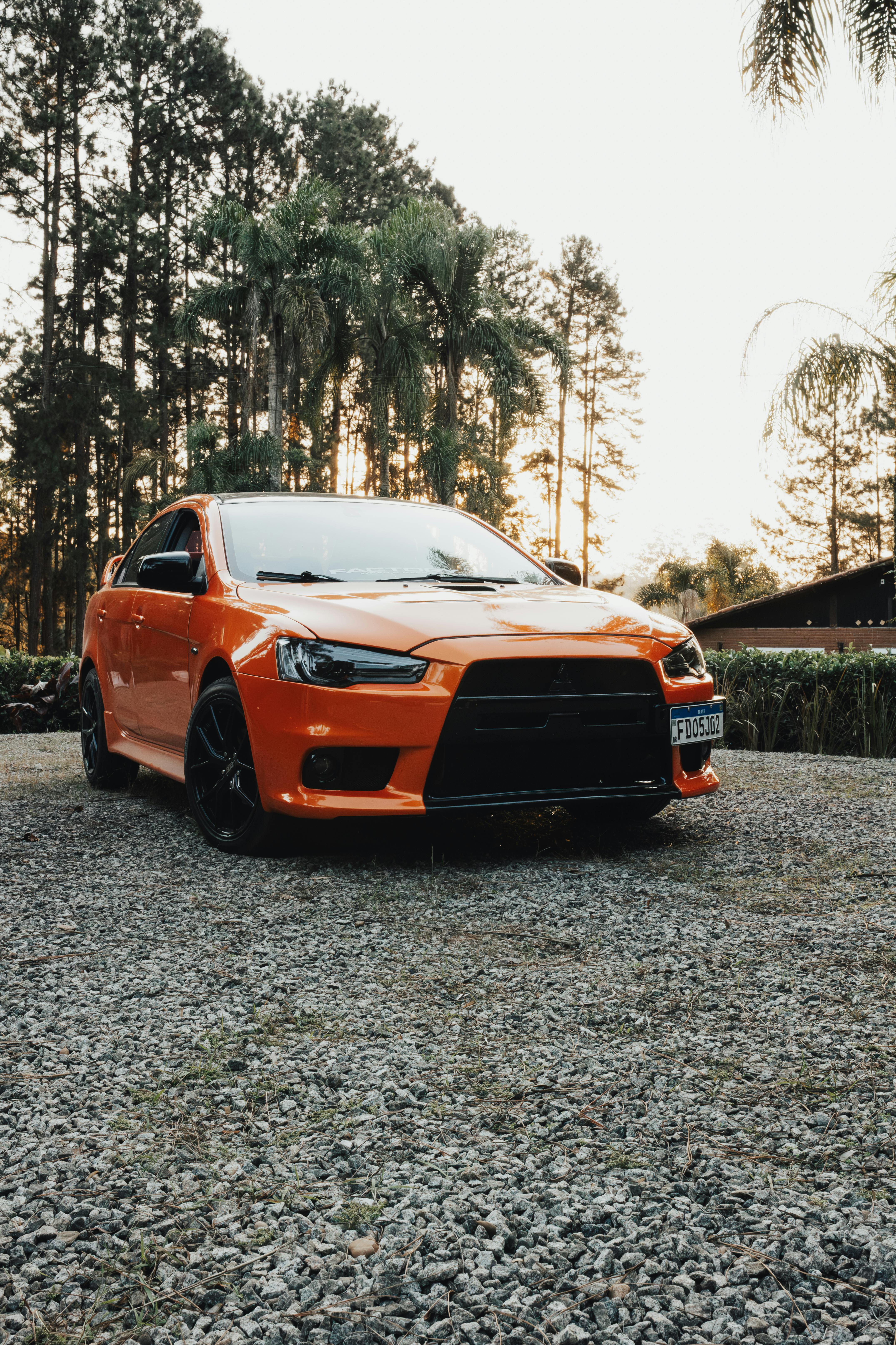 Orange Mitsubishi Lancer in a Gravel Parking Lot · Free Stock Photo