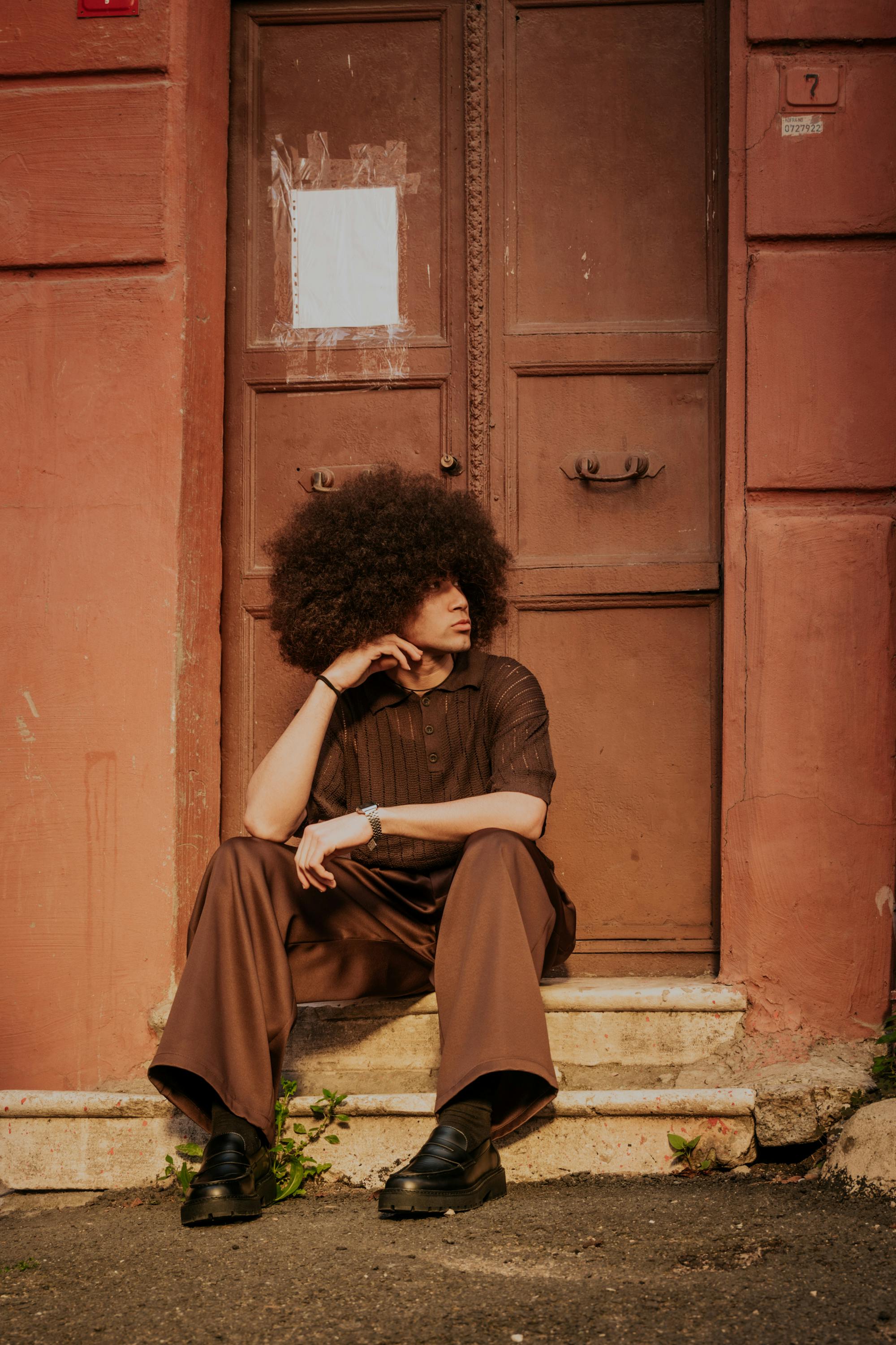 Portrait of a Young Man Wearing an Afro Sitting on Steps · Free Stock Photo