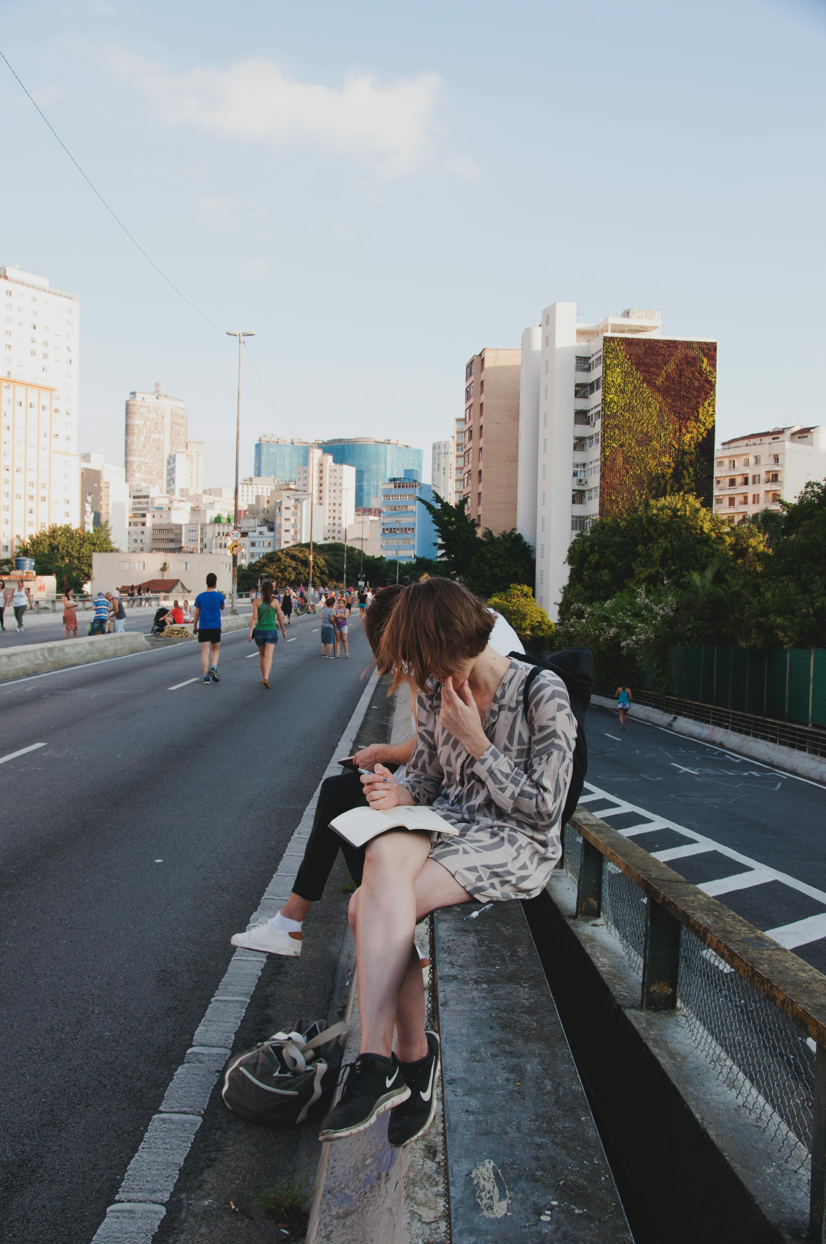 Woman Sitting on Railings Under Grey Clouds · Free Stock Photo