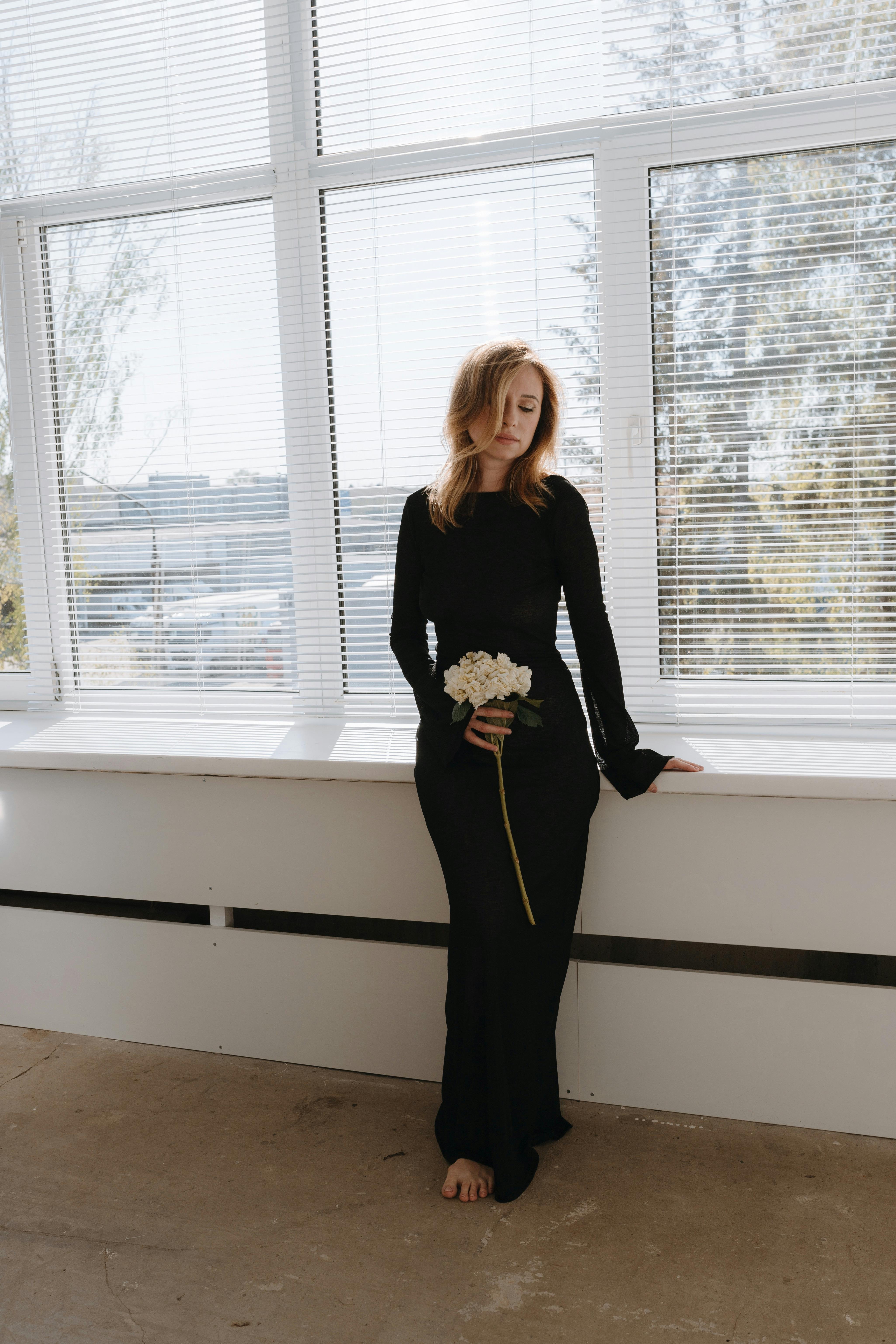 Woman in Black Dress Standing under Window Panel Holding White Flowers ...