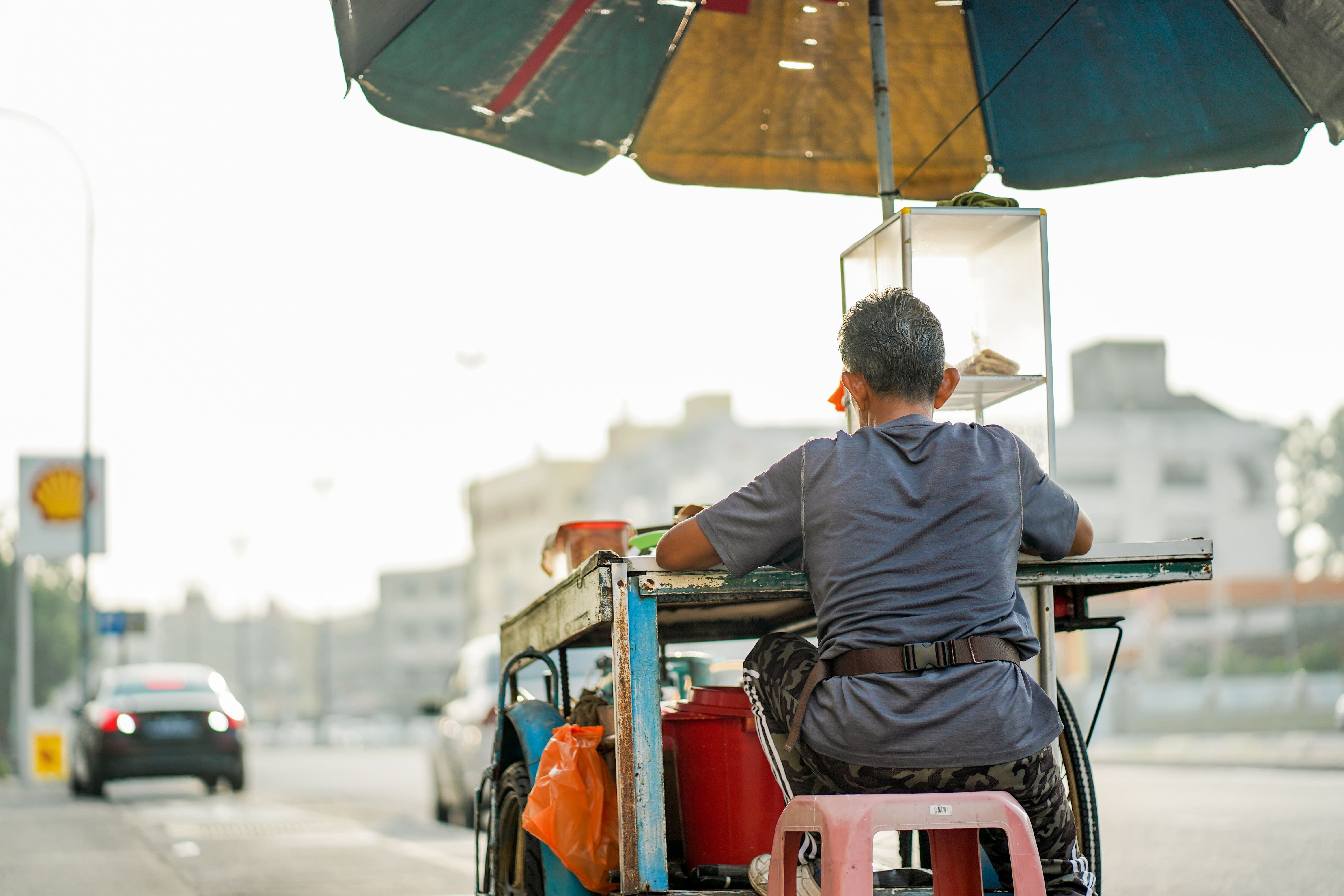 Elderly Street Vendor Sitting at Table · Free Stock Photo