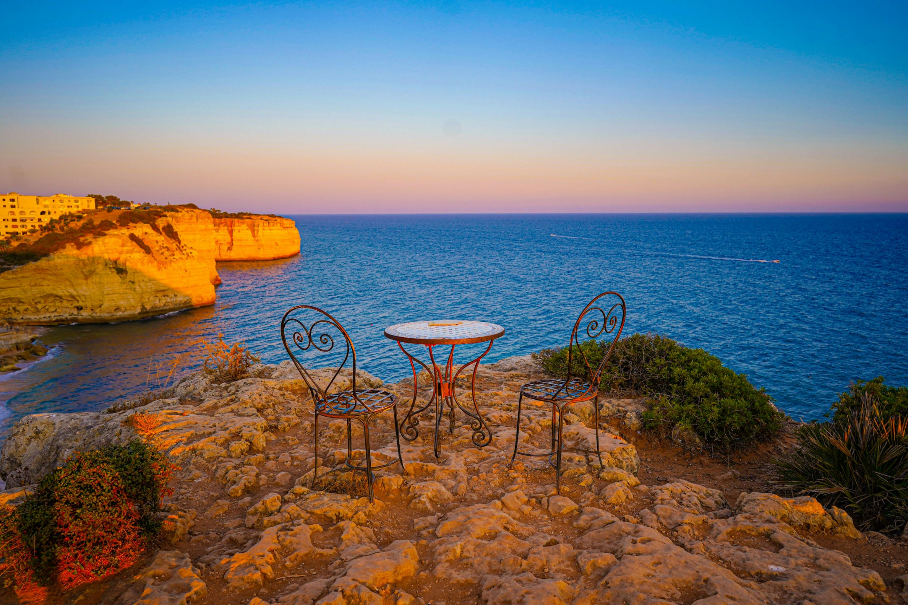 A Table and Chairs Standing on the Cliff with View of the Ocean at Sunset, Algarve, Portugal ...