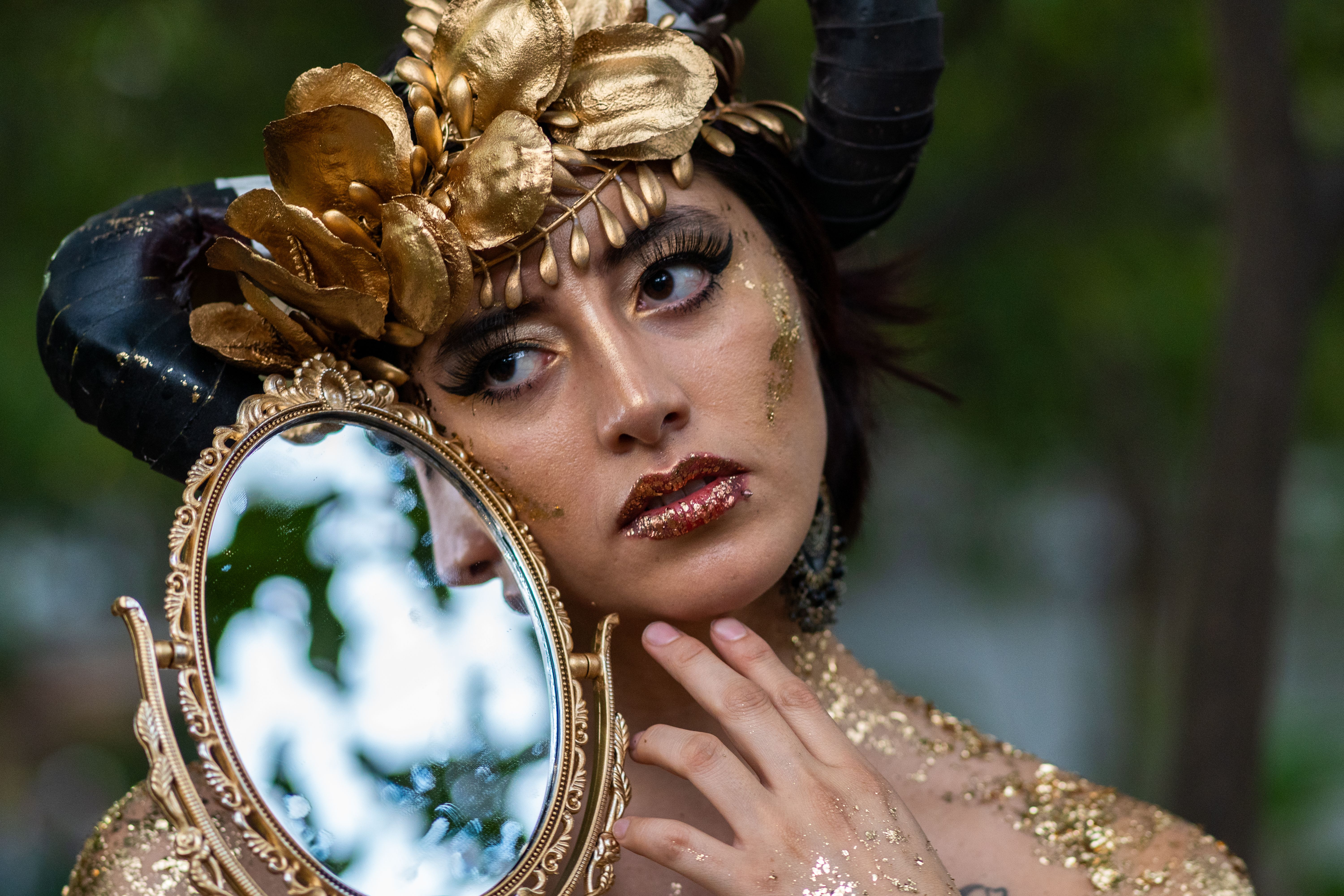 A woman with horns and gold makeup holding a mirror · Free Stock Photo