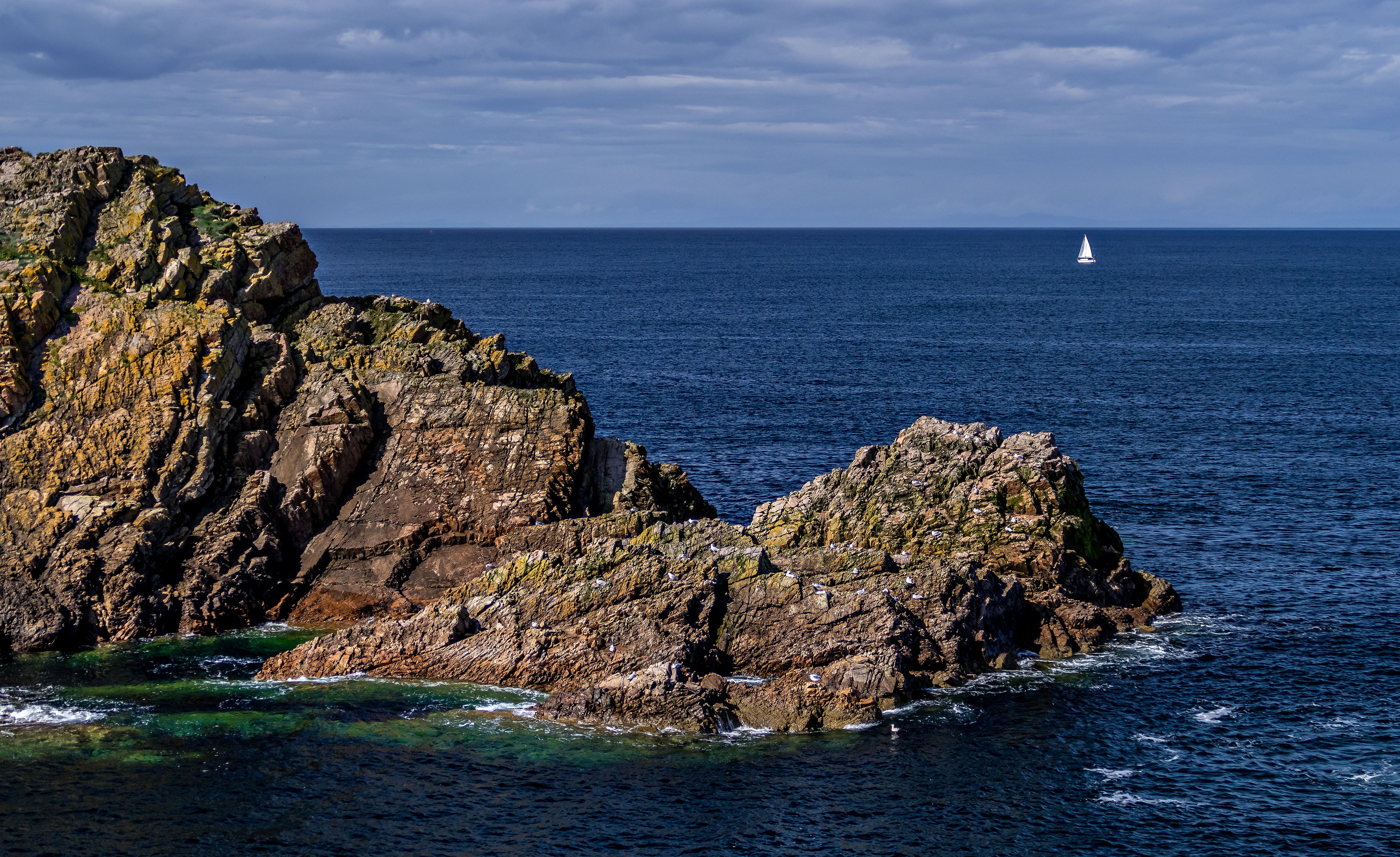 Rocks on Sea Shore and Sailboat behind · Free Stock Photo
