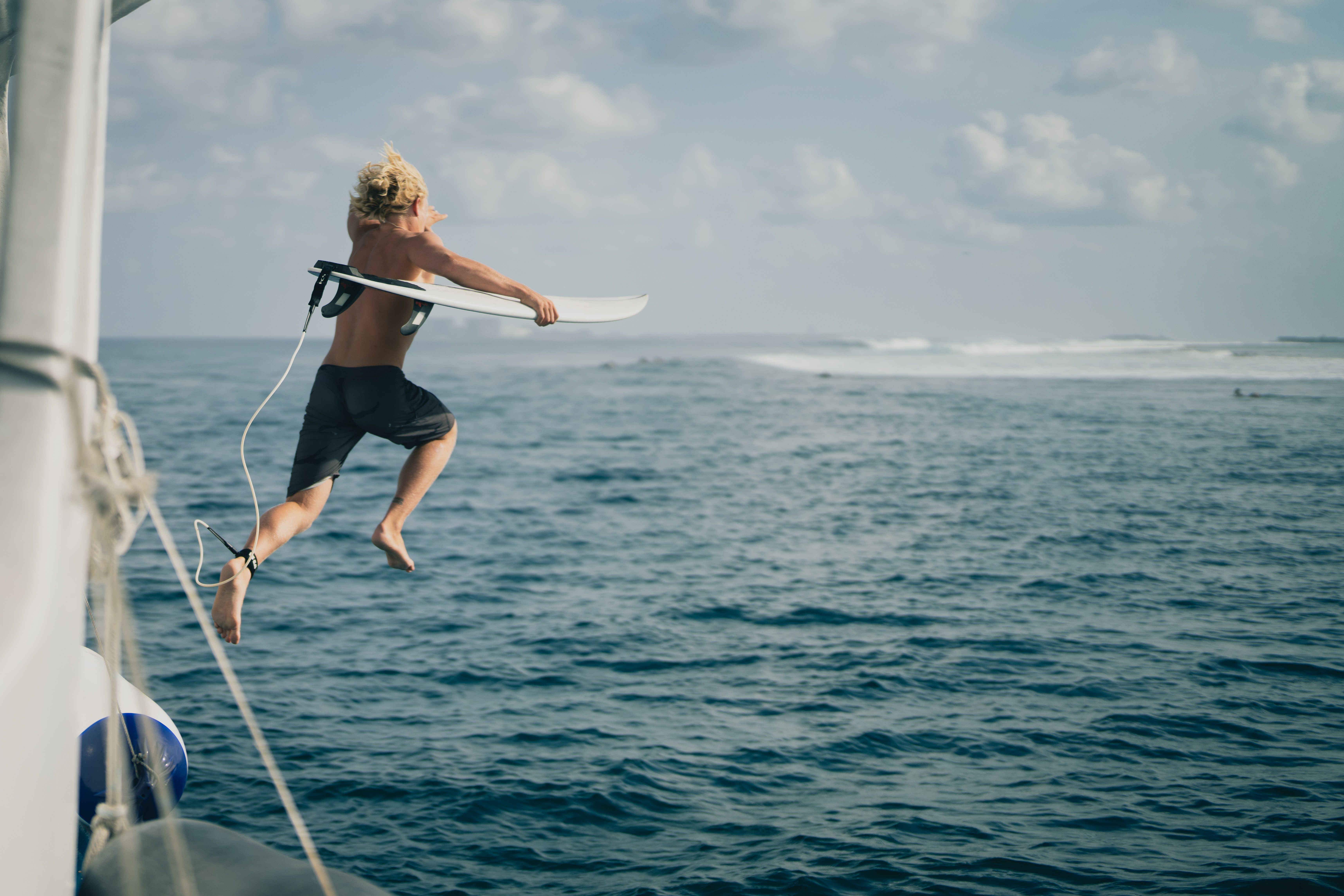 A Man Jumping from a Boat into the Sea with a Board · Free Stock Photo