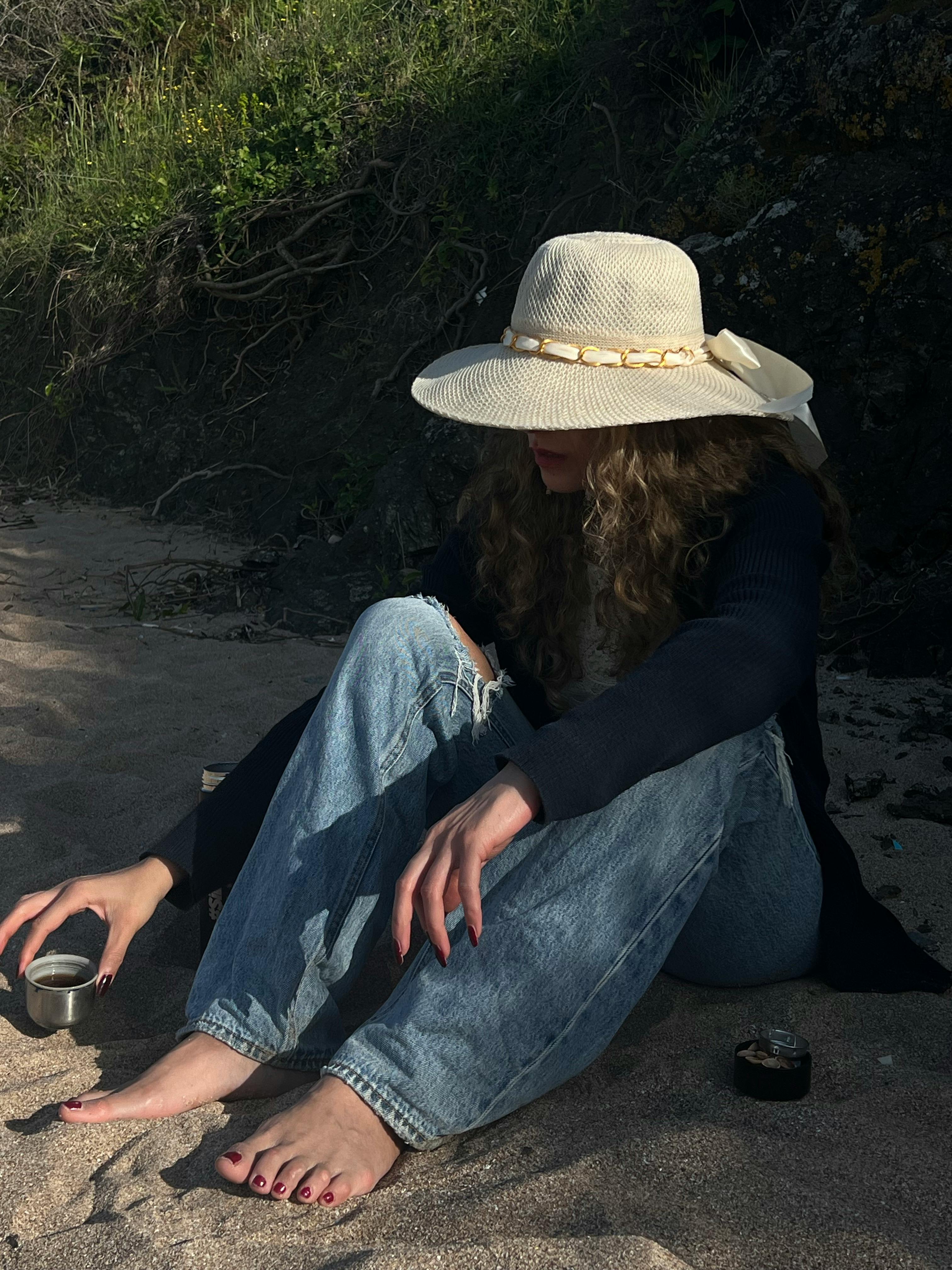 Woman Wearing Large Hat Black Blouse and Jeans Sitting on Sand Reaching ...