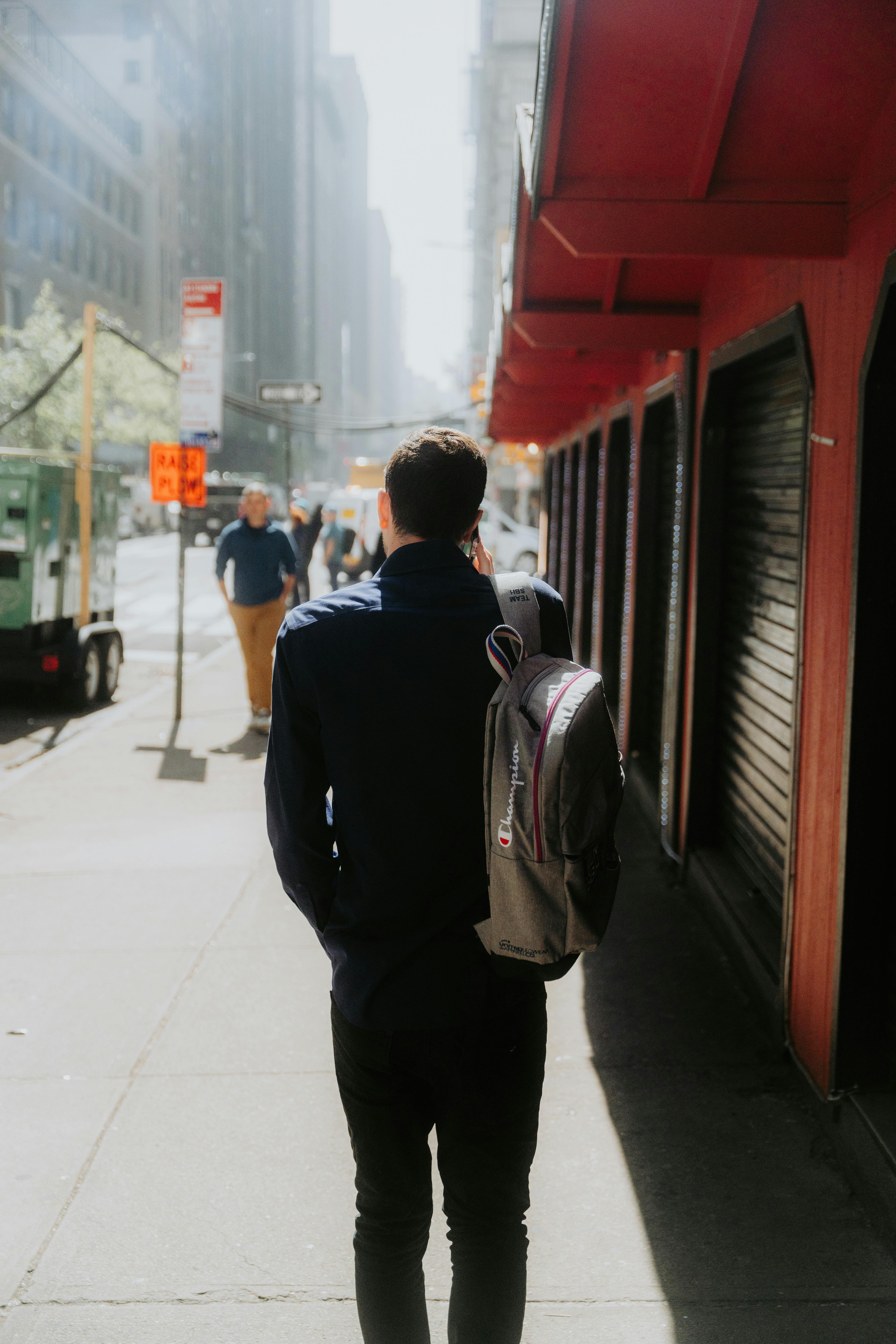 Man Walking with Backpack on Sidewalk · Free Stock Photo