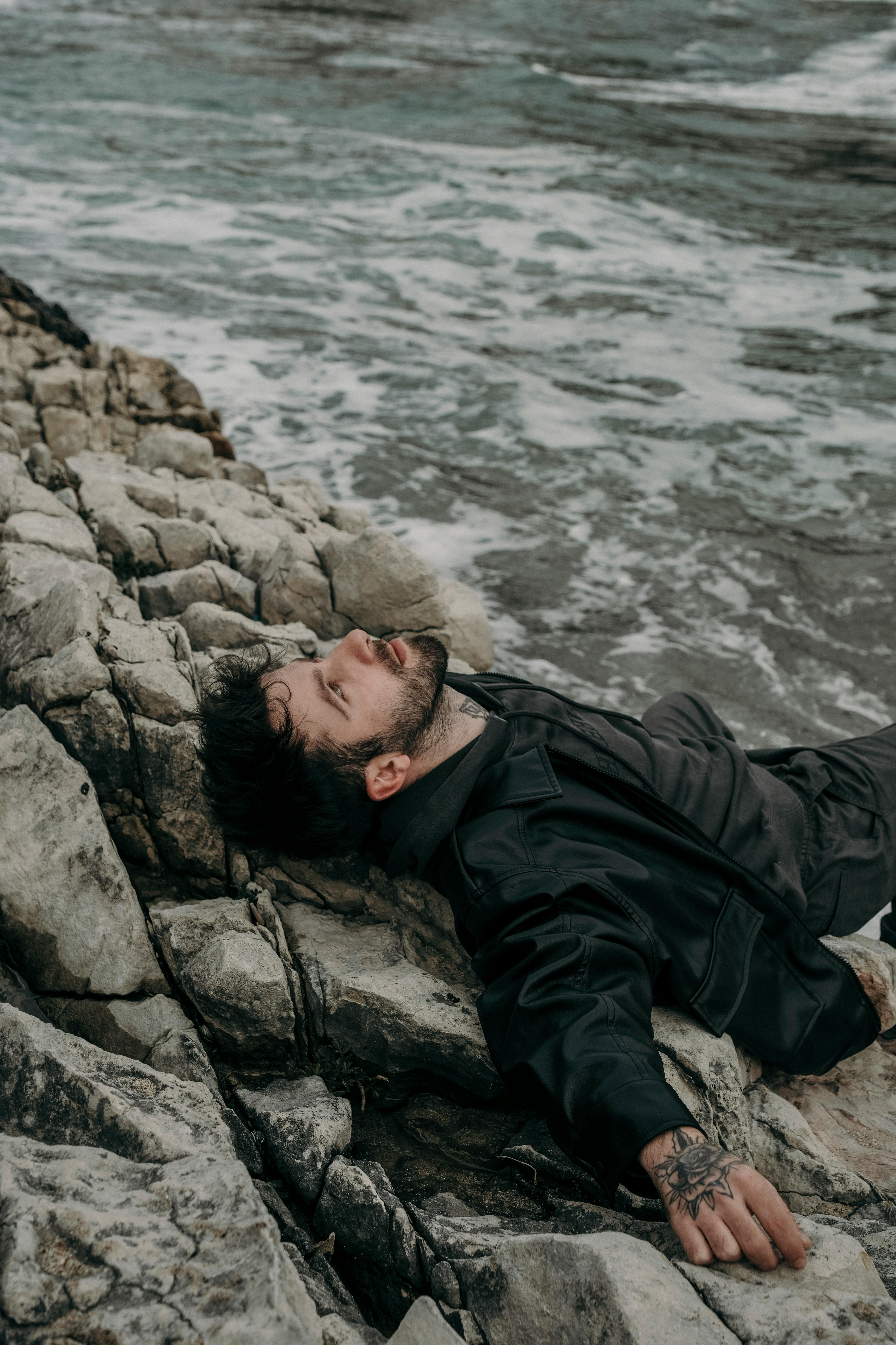 Man in Black Jacket Lying Down on Rocks by River · Free Stock Photo