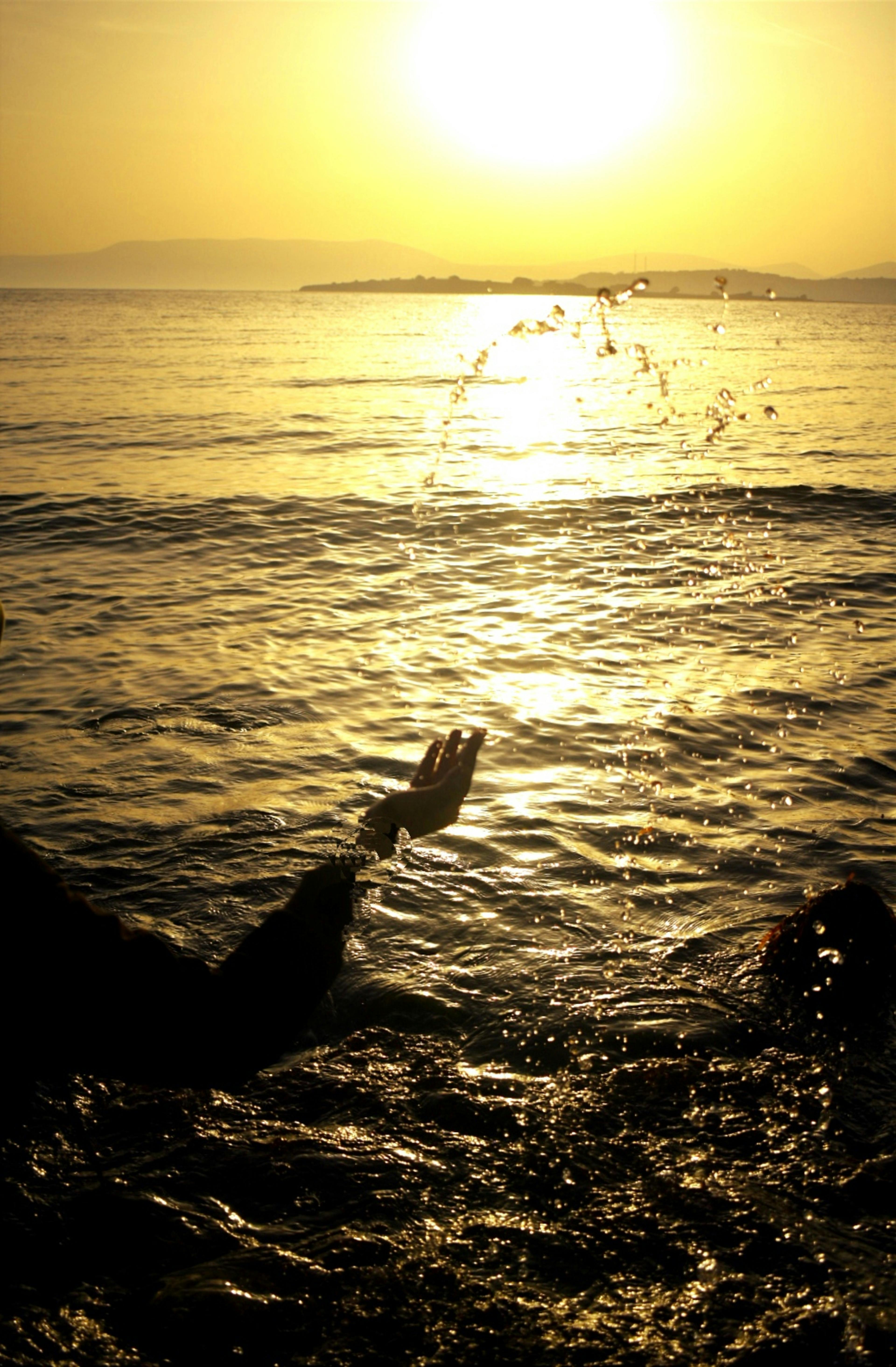 Person Hand Throwing Water on Sea Shore at Sunset · Free Stock Photo