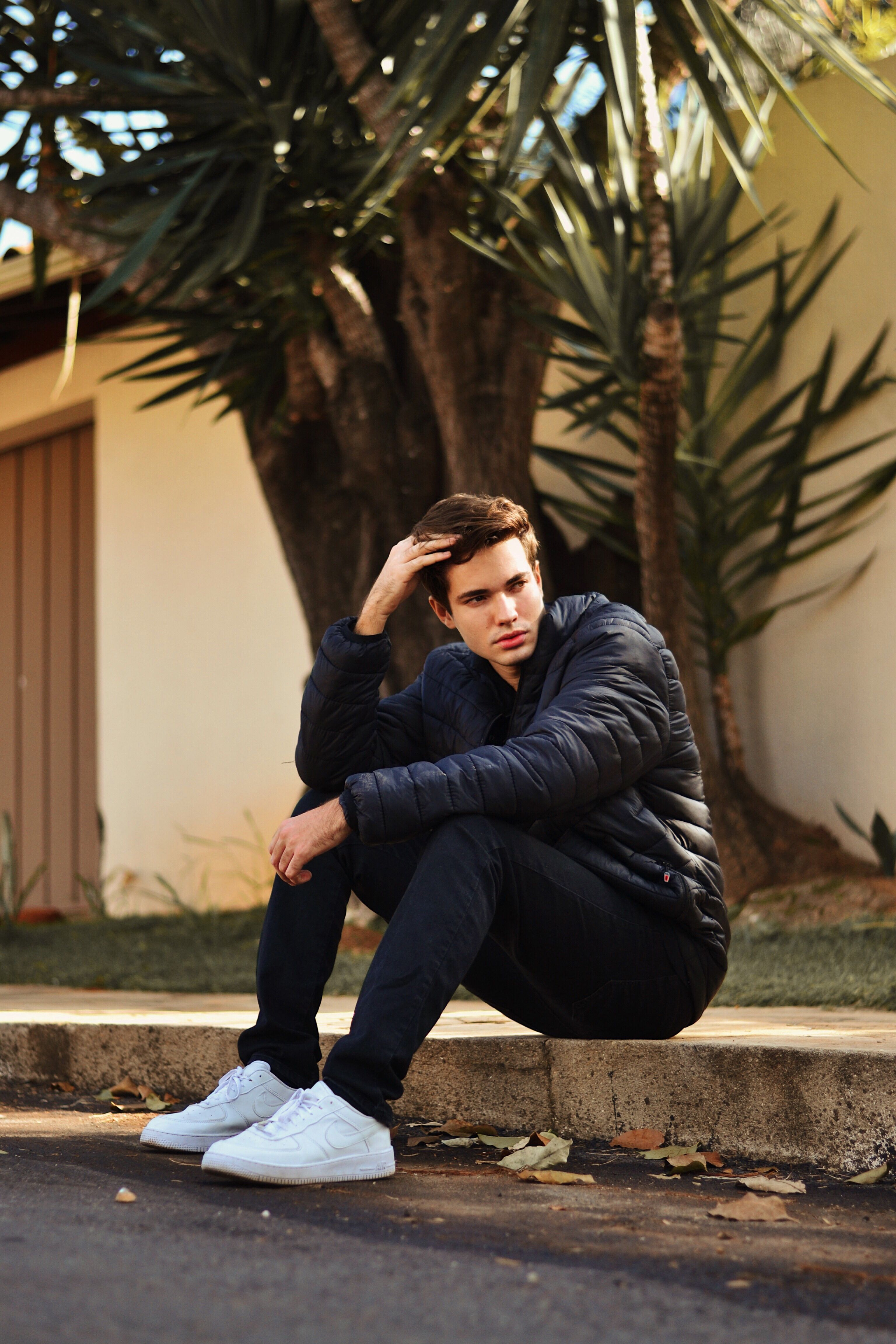 A young man sitting on the curb in front of a building · Free Stock Photo