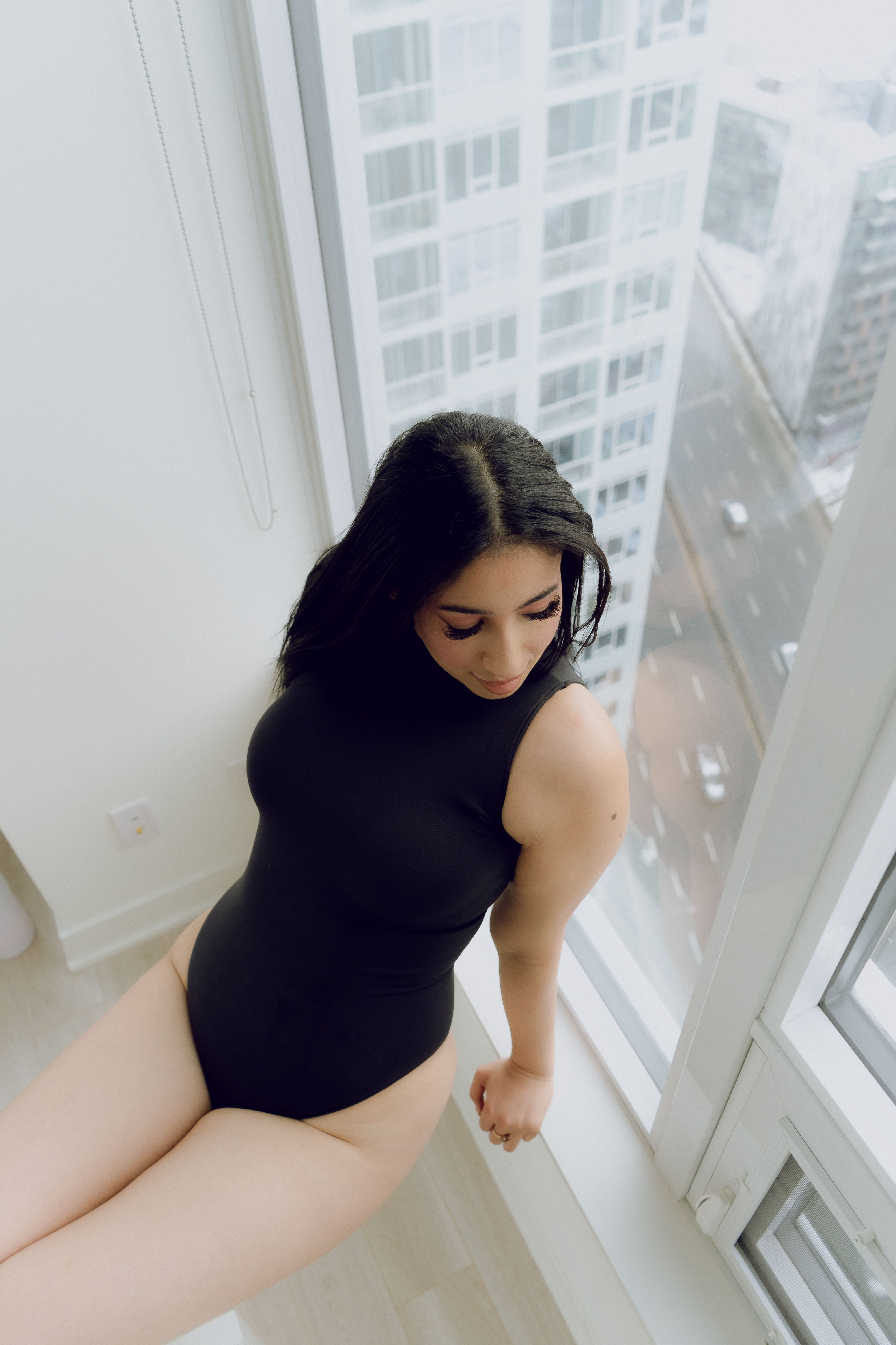 A woman in a black bodysuit sitting on a window sill · Free Stock Photo