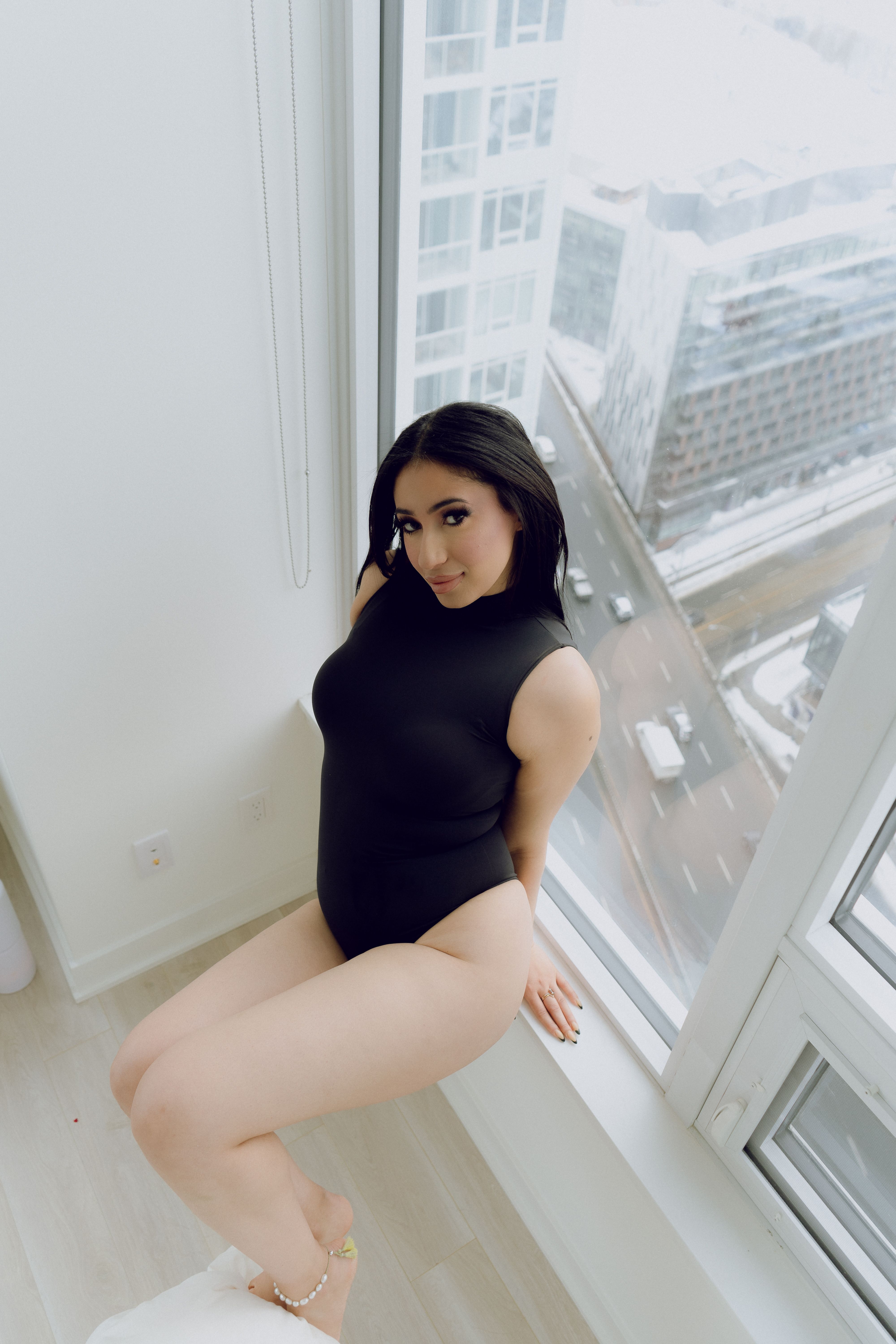 A woman in a black bodysuit sitting on a window sill · Free Stock Photo