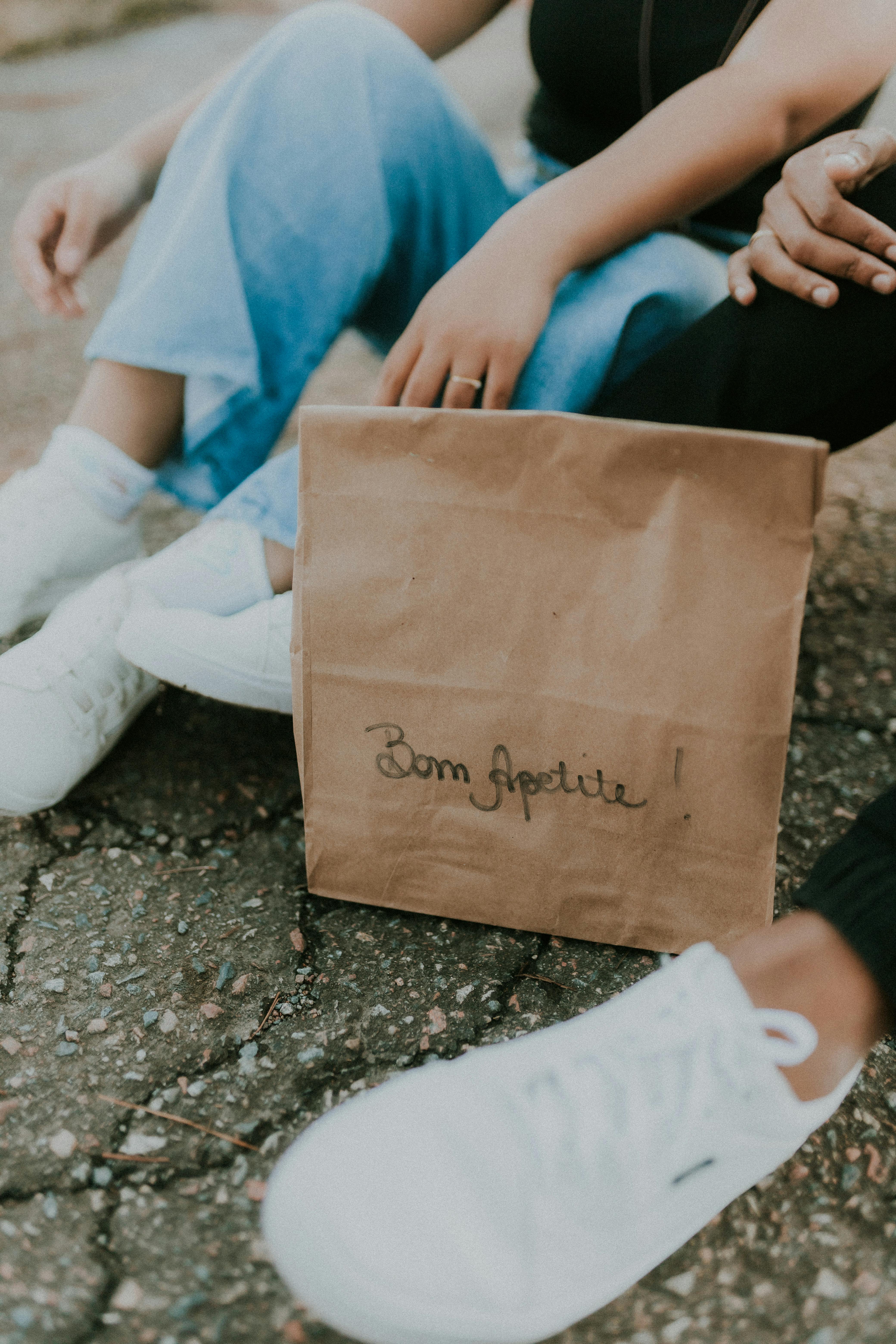 Legs of People Sitting in Front of a Paper Bag · Free Stock Photo
