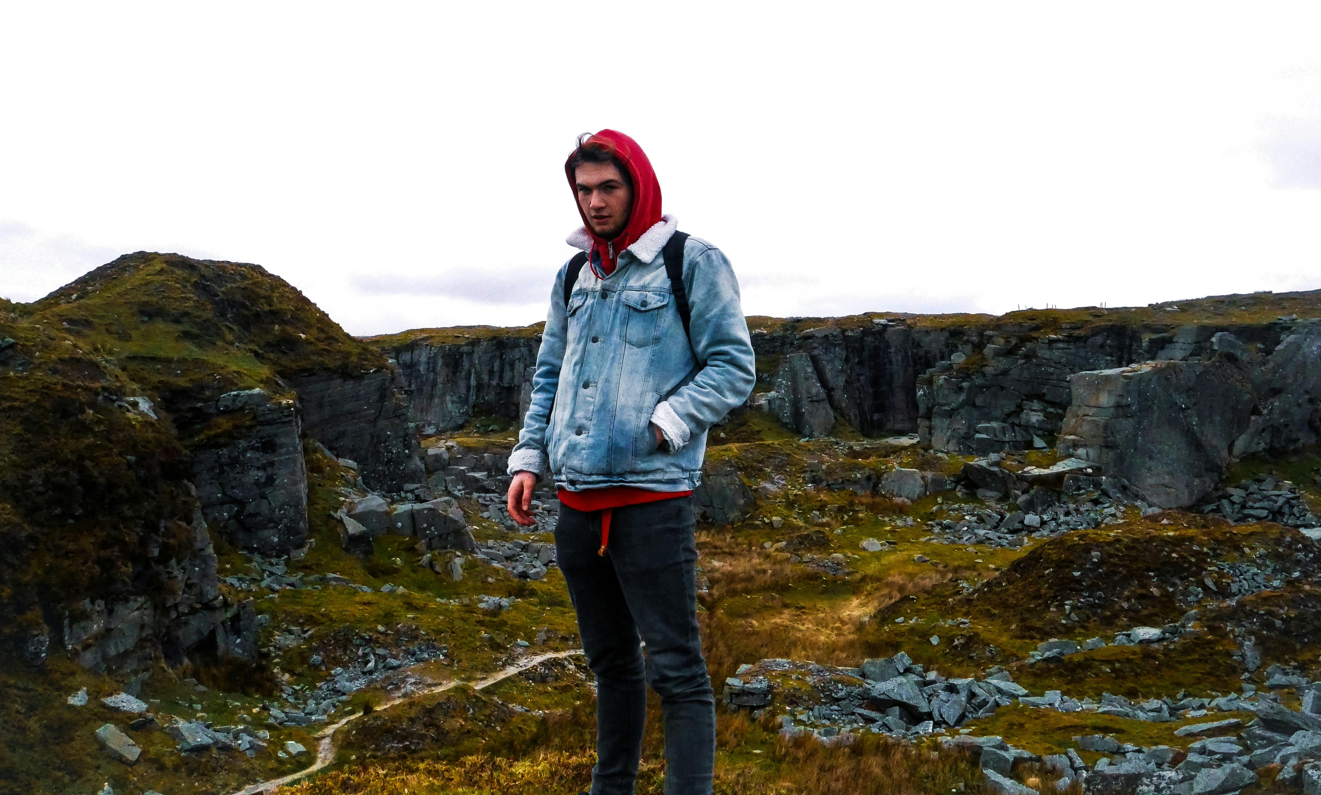 Photo of a man wearing a denim jacket standing on rocky landscape ...