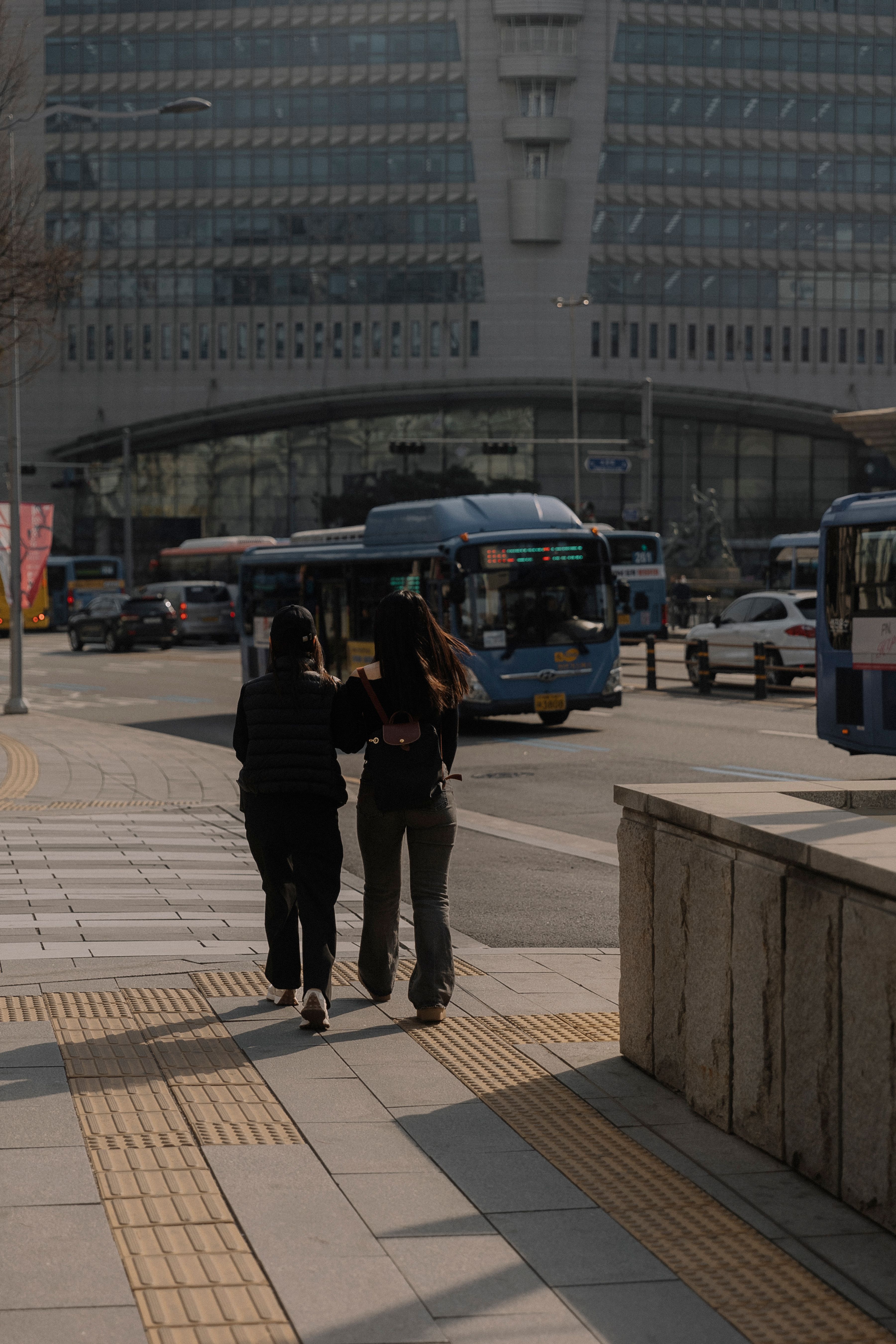 Two people walking down a sidewalk in front of a bus · Free Stock Photo
