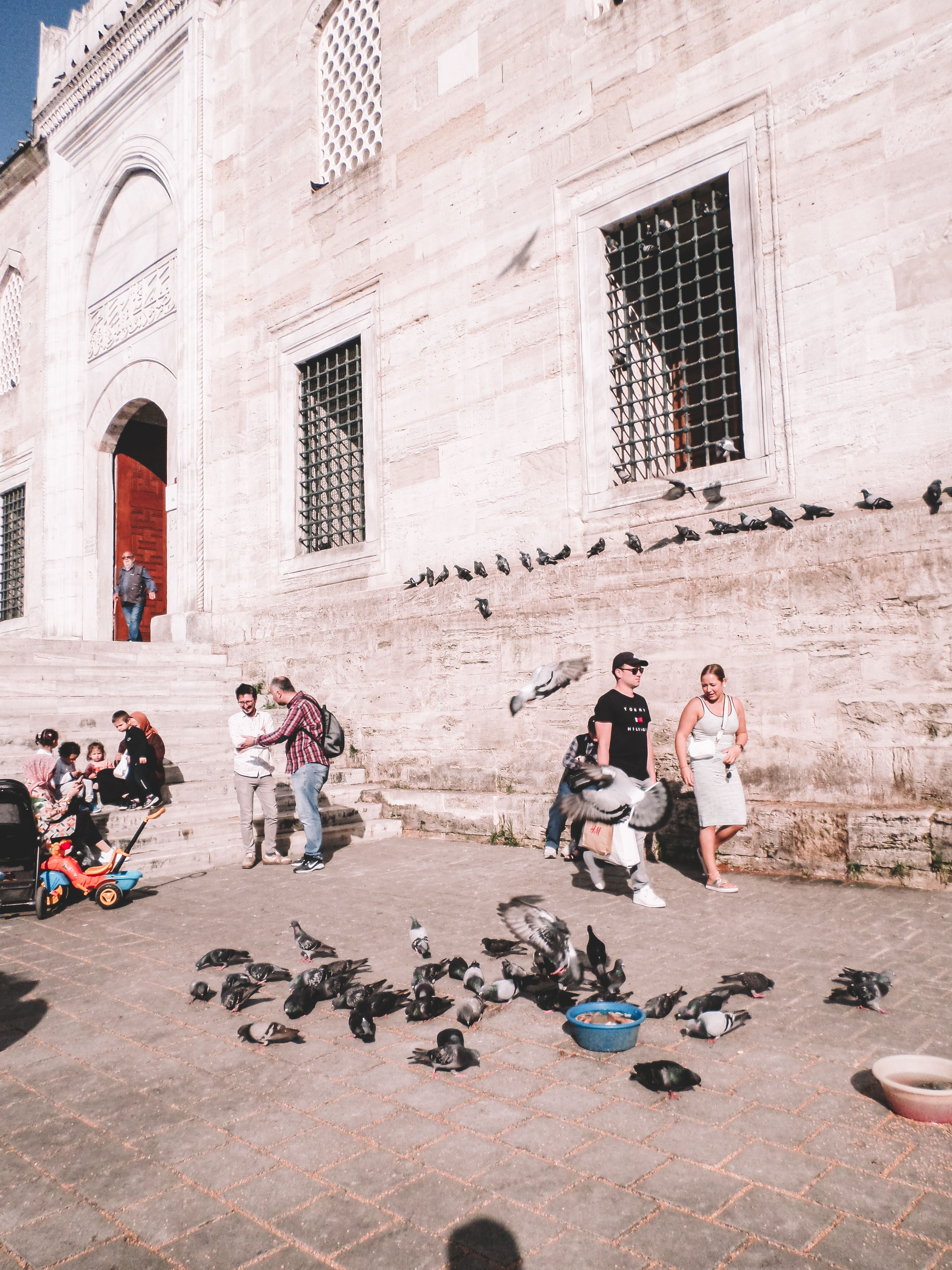 A group of people standing around a building with pigeons · Free Stock ...